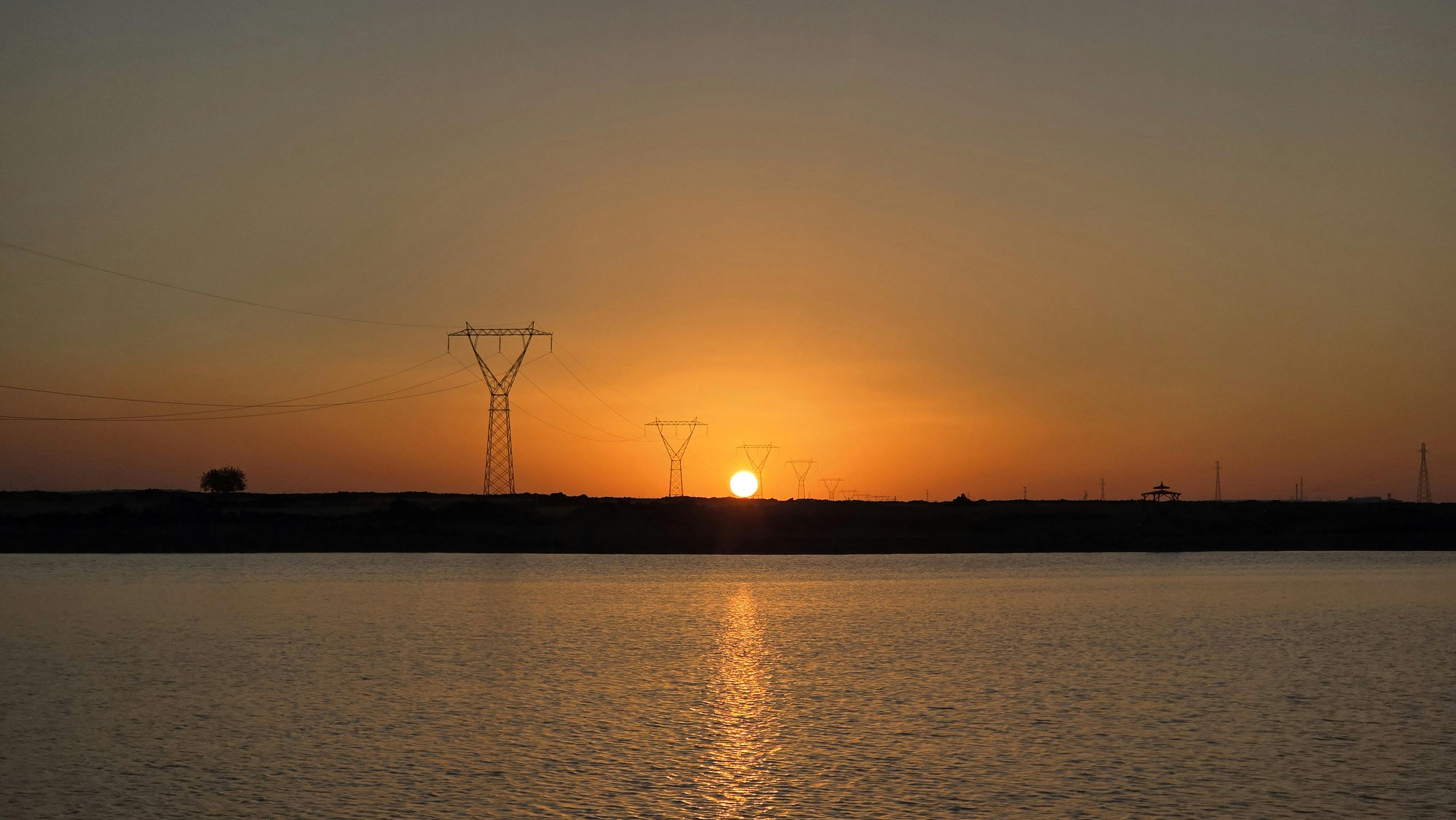 Scenic Sunset Over Water and Power Lines · Free Stock Photo