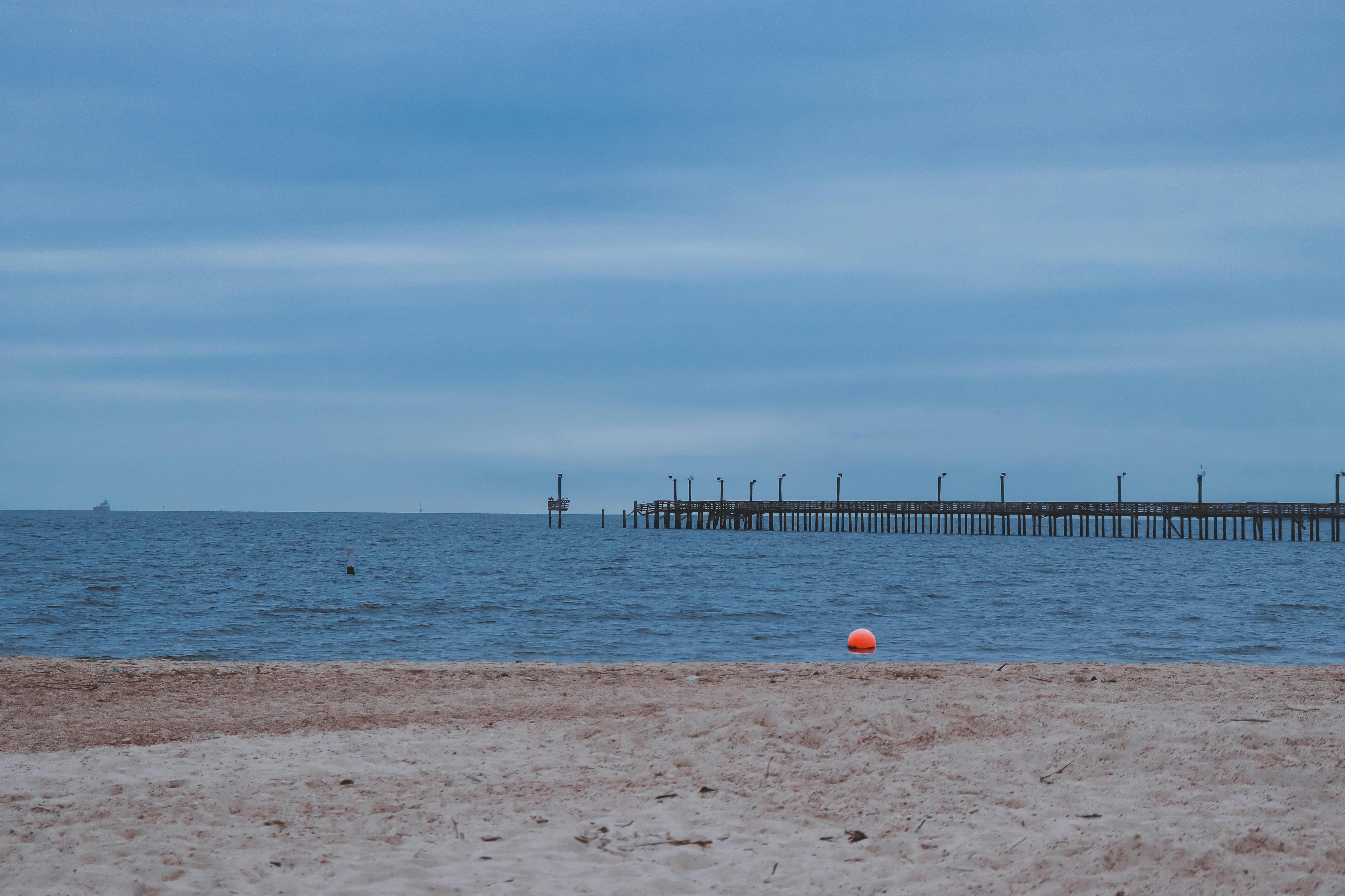 Serene Beachfront View with Pier and Buoy · Free Stock Photo