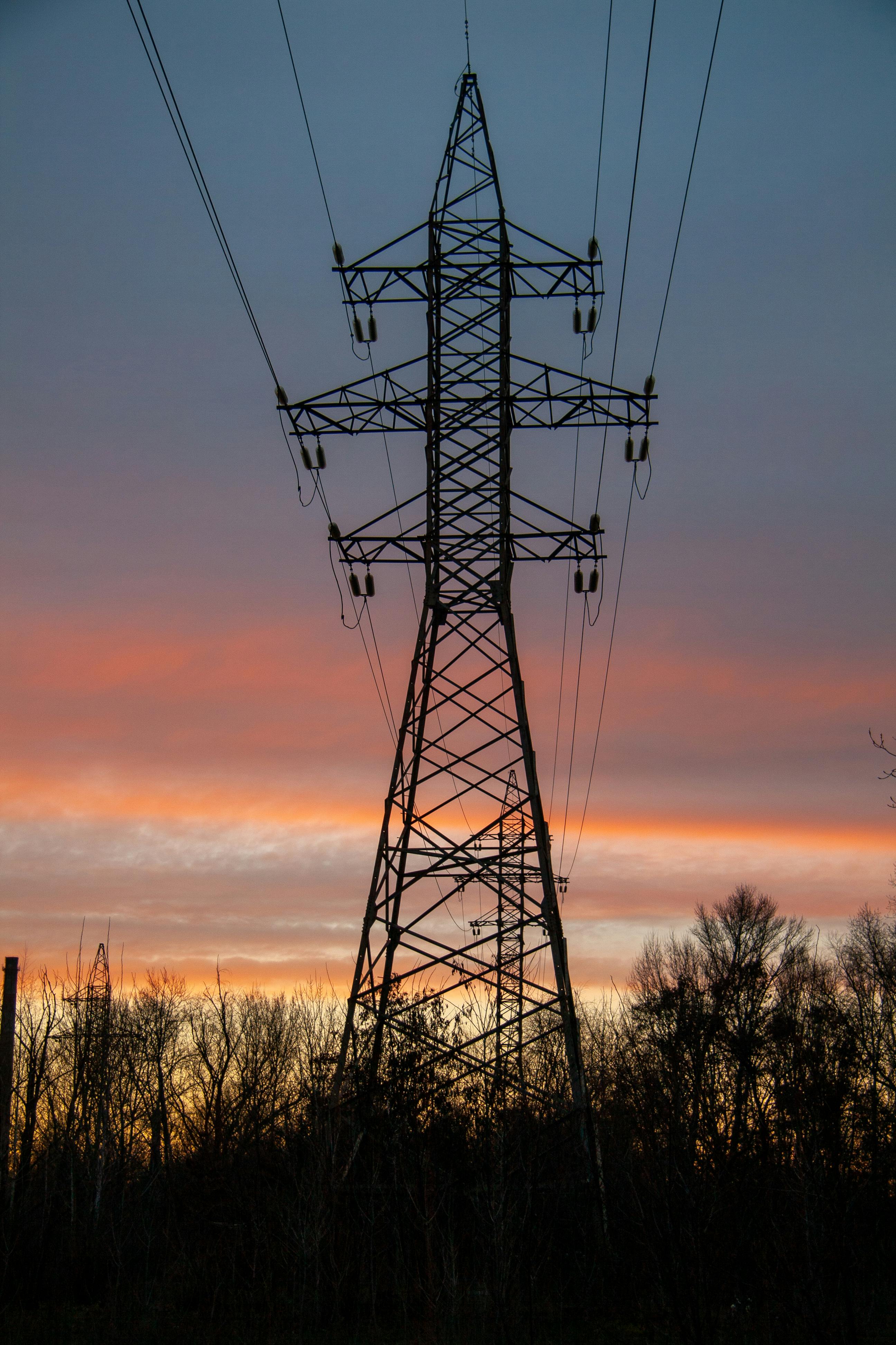 Powerline Tower at Sunset with Silhouetted Trees · Free Stock Photo