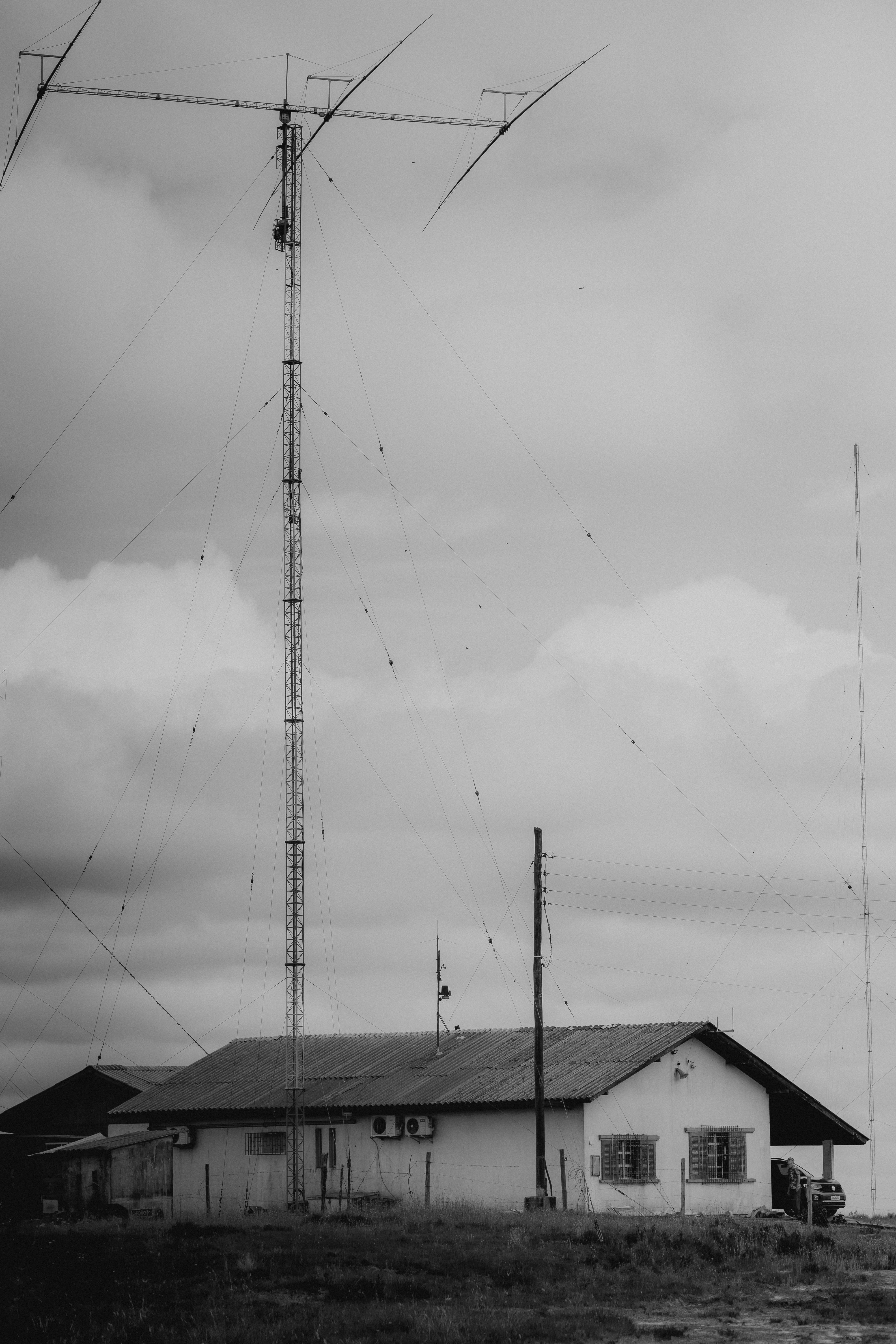Tall radio tower beside rural house in grayscale · Free Stock Photo
