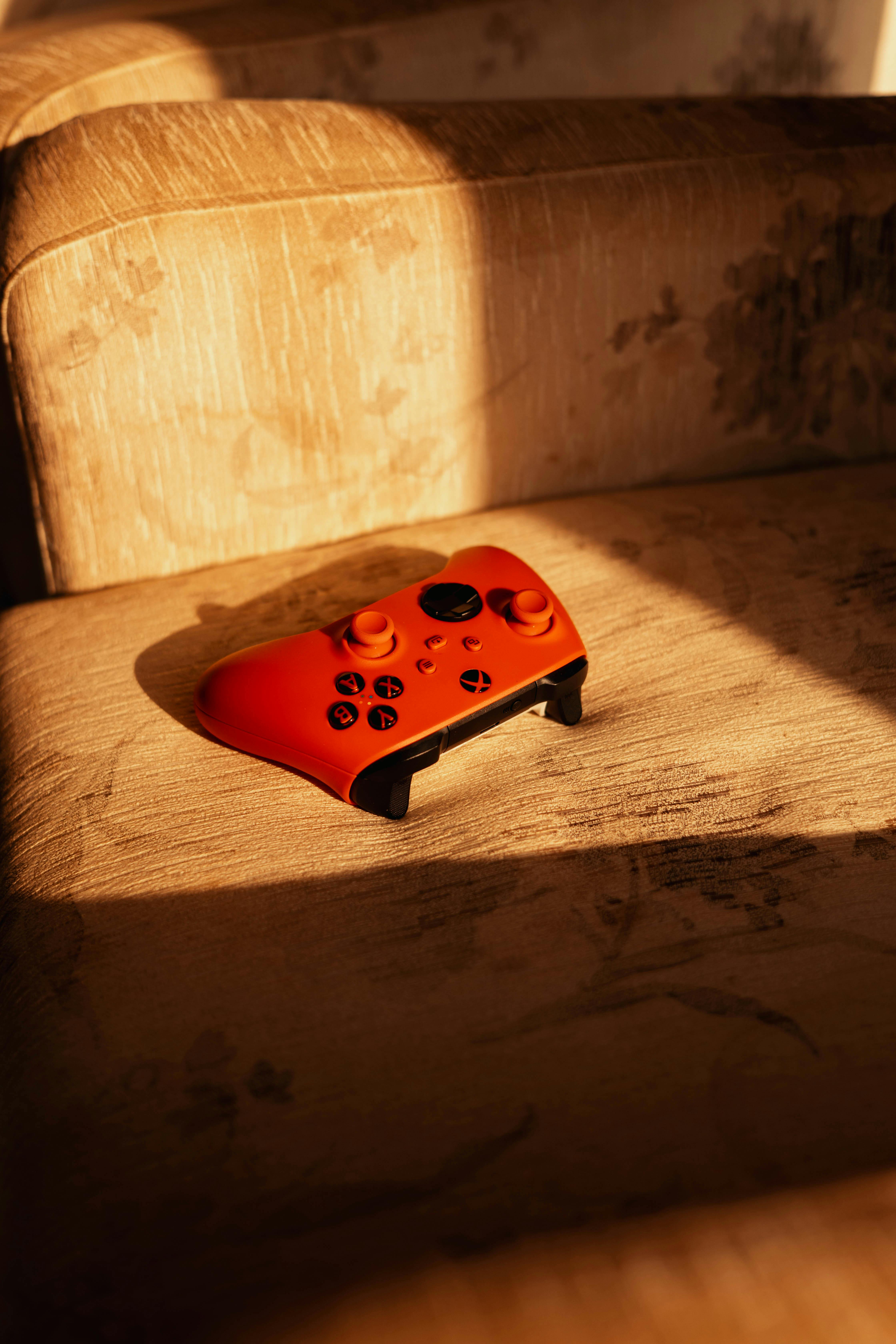 Vibrant Red Gaming Controller on Sofa in Sunlight · Free Stock Photo