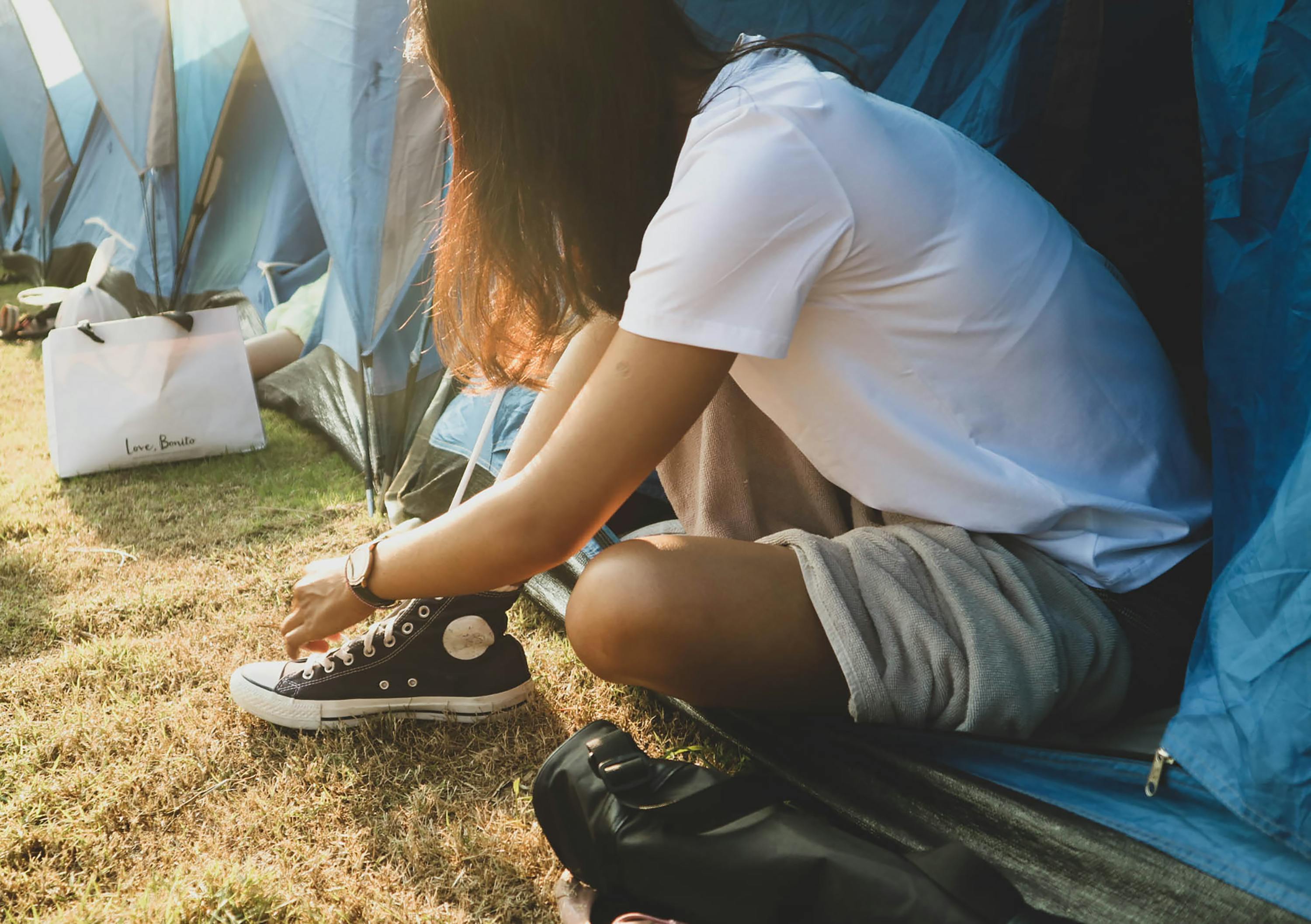 Anonymous woman tying shoelaces near tent · Free Stock Photo