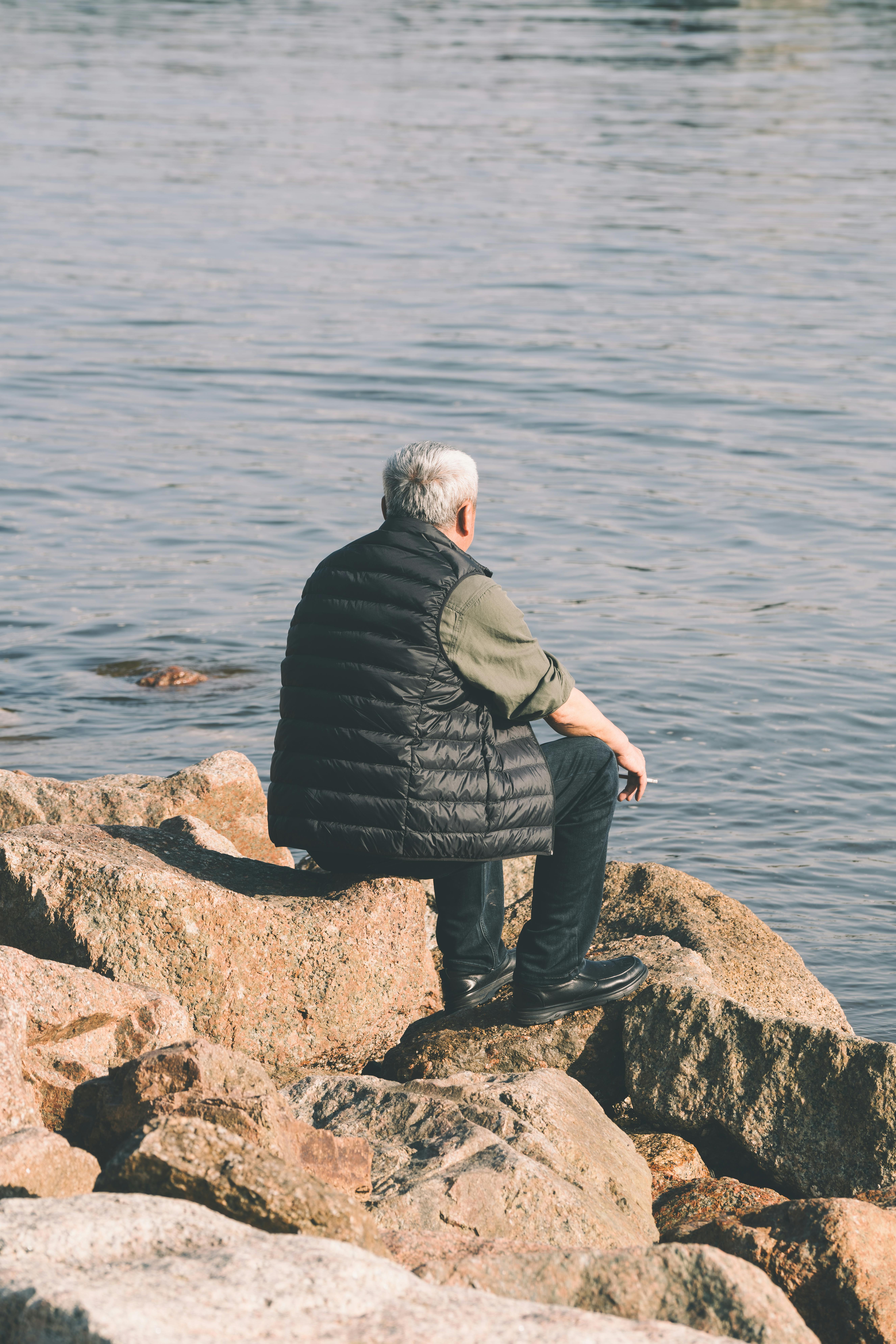 Elderly Man Reflecting by Seaside Rocks · Free Stock Photo