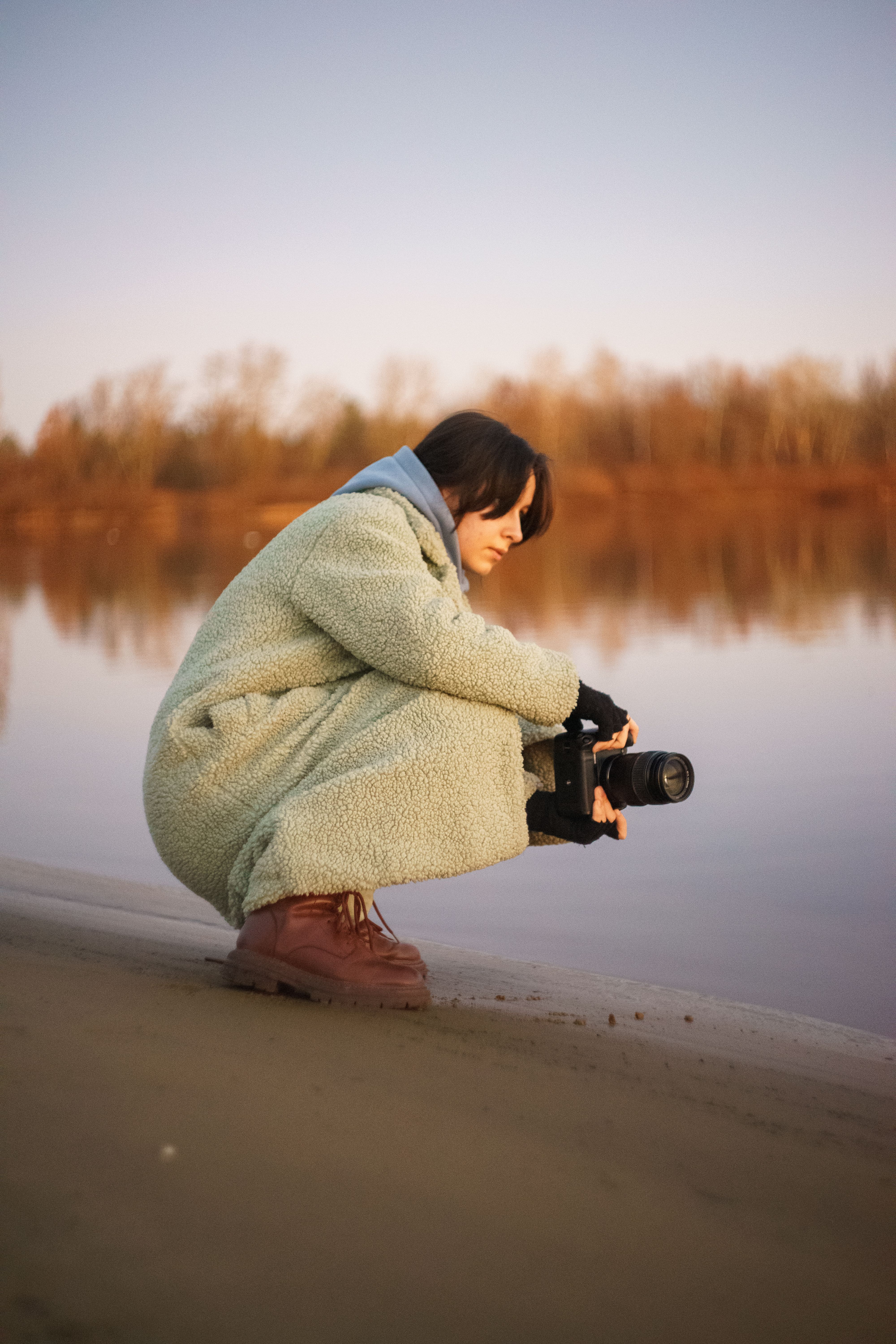 Photographer Squatting by Riverbank at Sunset · Free Stock Photo