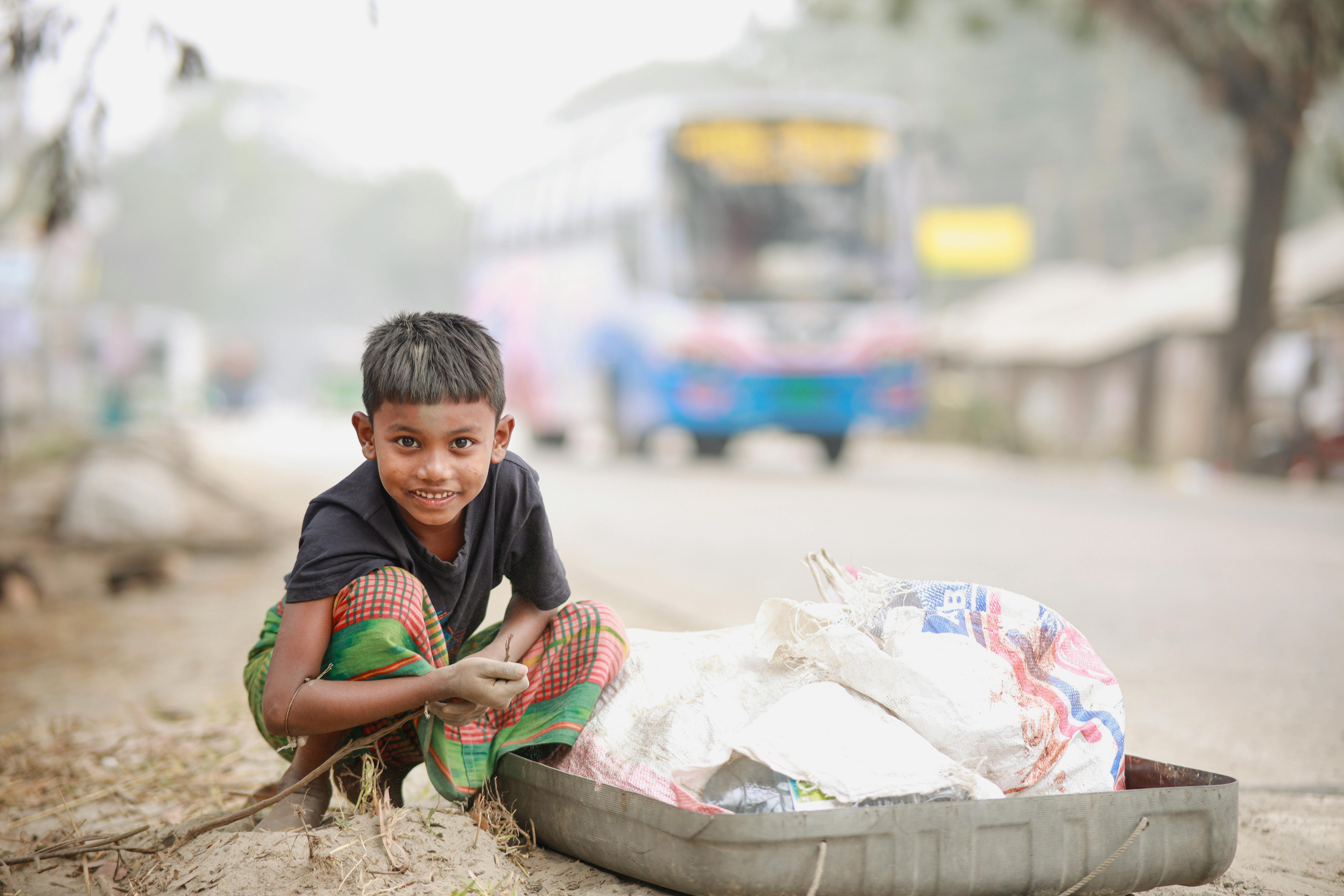 Smiling Child Collecting Materials on a Busy Street · Free Stock Photo