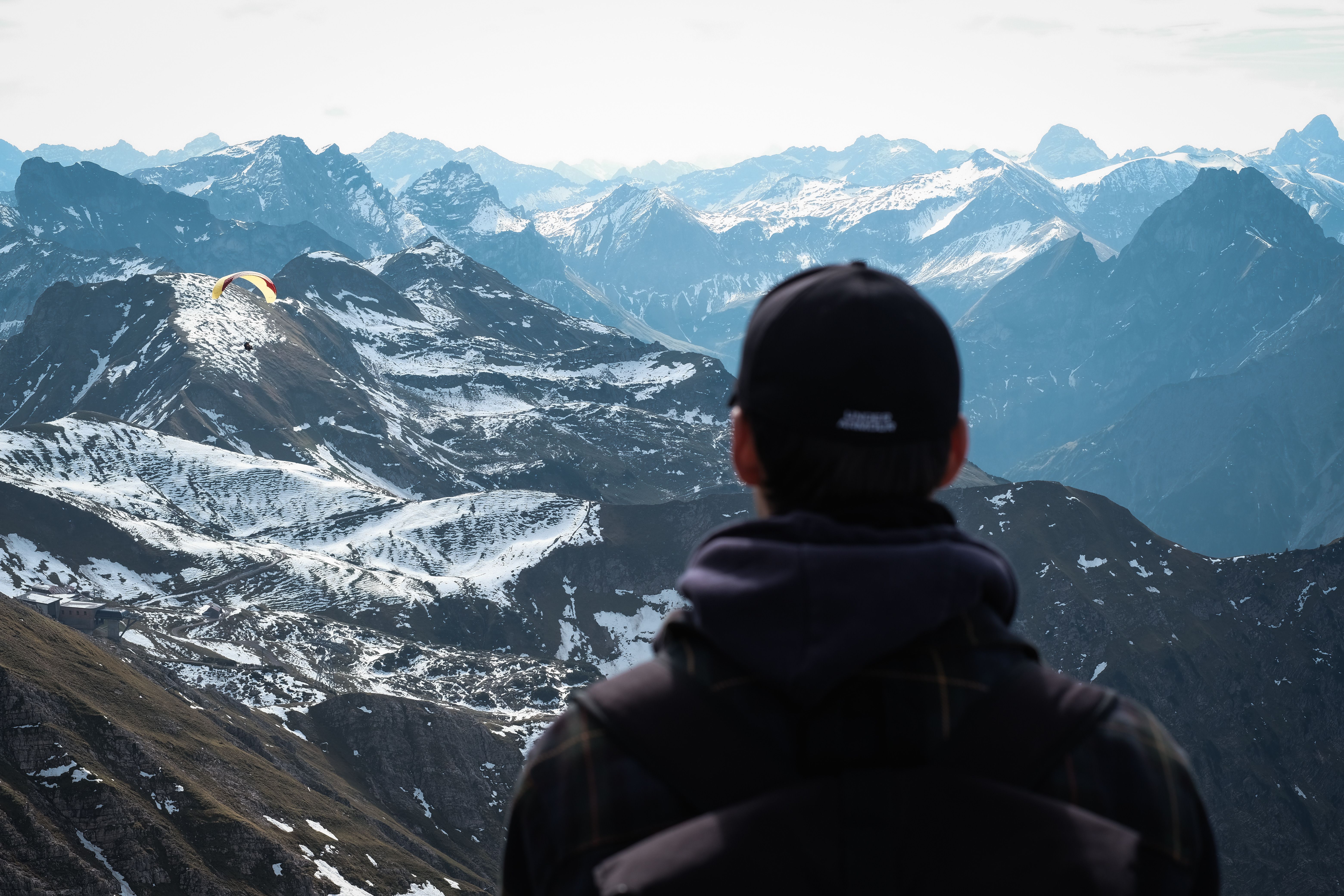 Person Admiring Snowy Mountains and Paraglider · Free Stock Photo