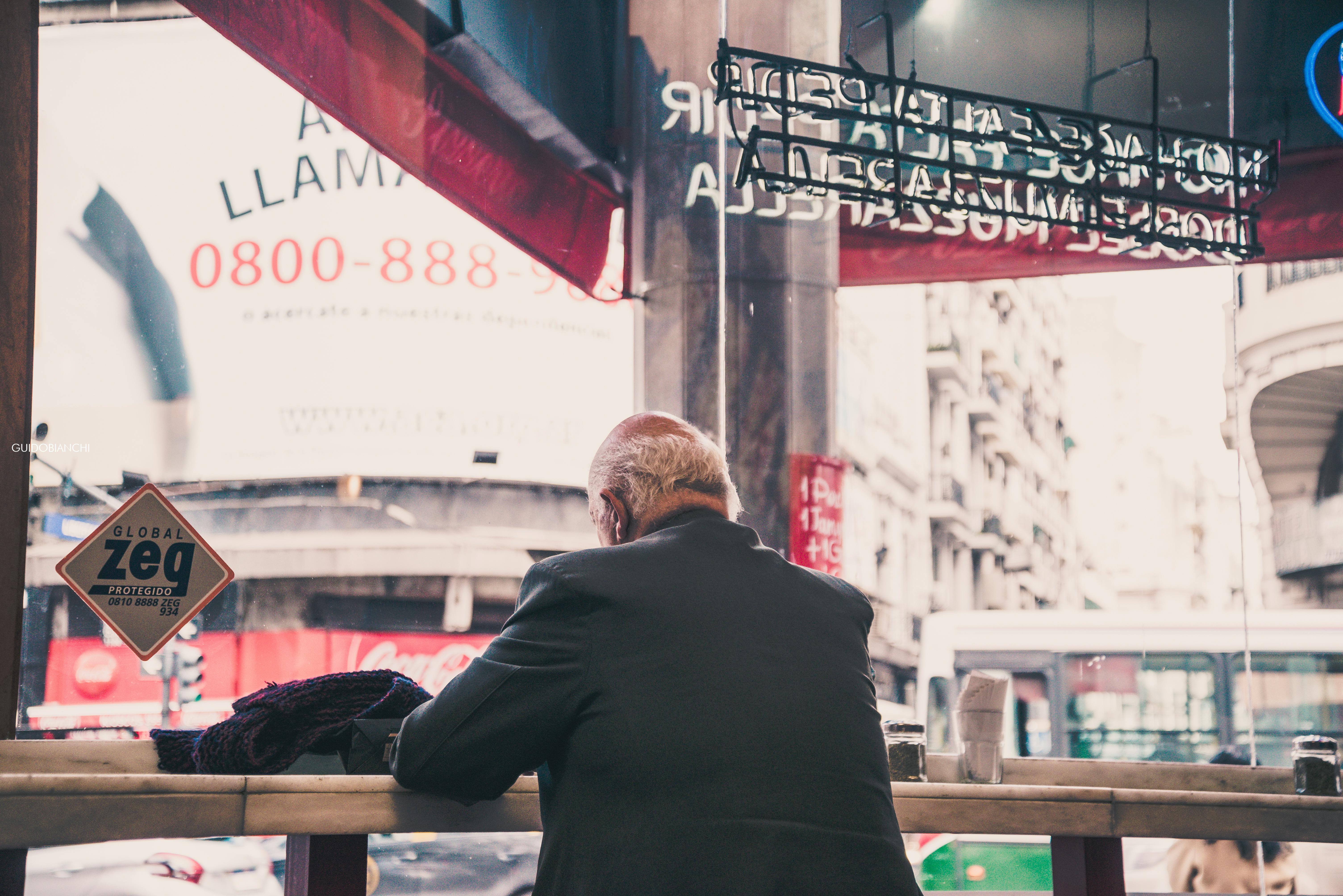 Elderly man gazing out café window in urban setting · Free Stock Photo