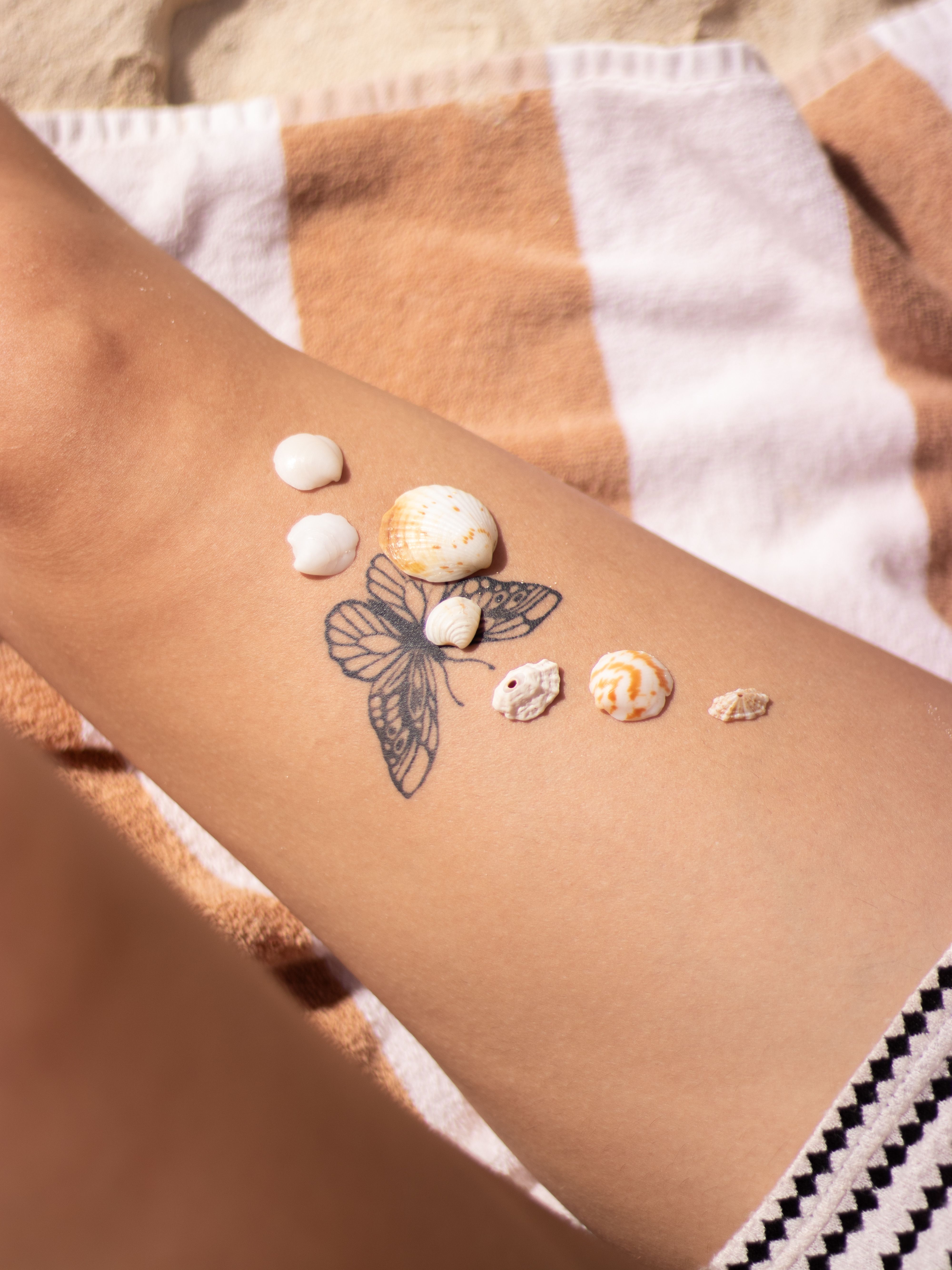 Tanned Leg with Butterfly Tattoo and Seashells on Beach · Free Stock Photo