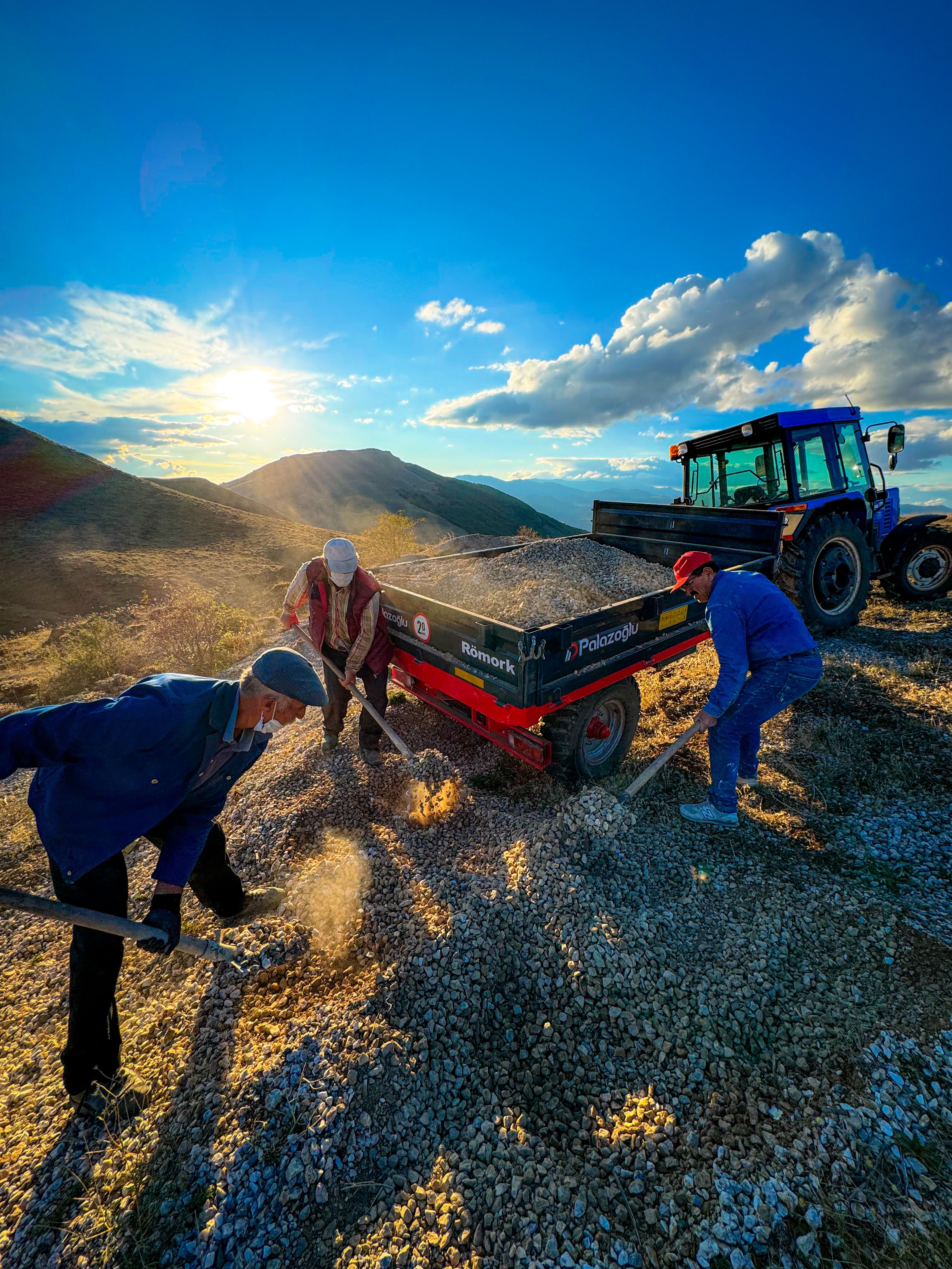 Farm Workers Using Tractor on Rocky Terrain at Sunset · Free Stock Photo