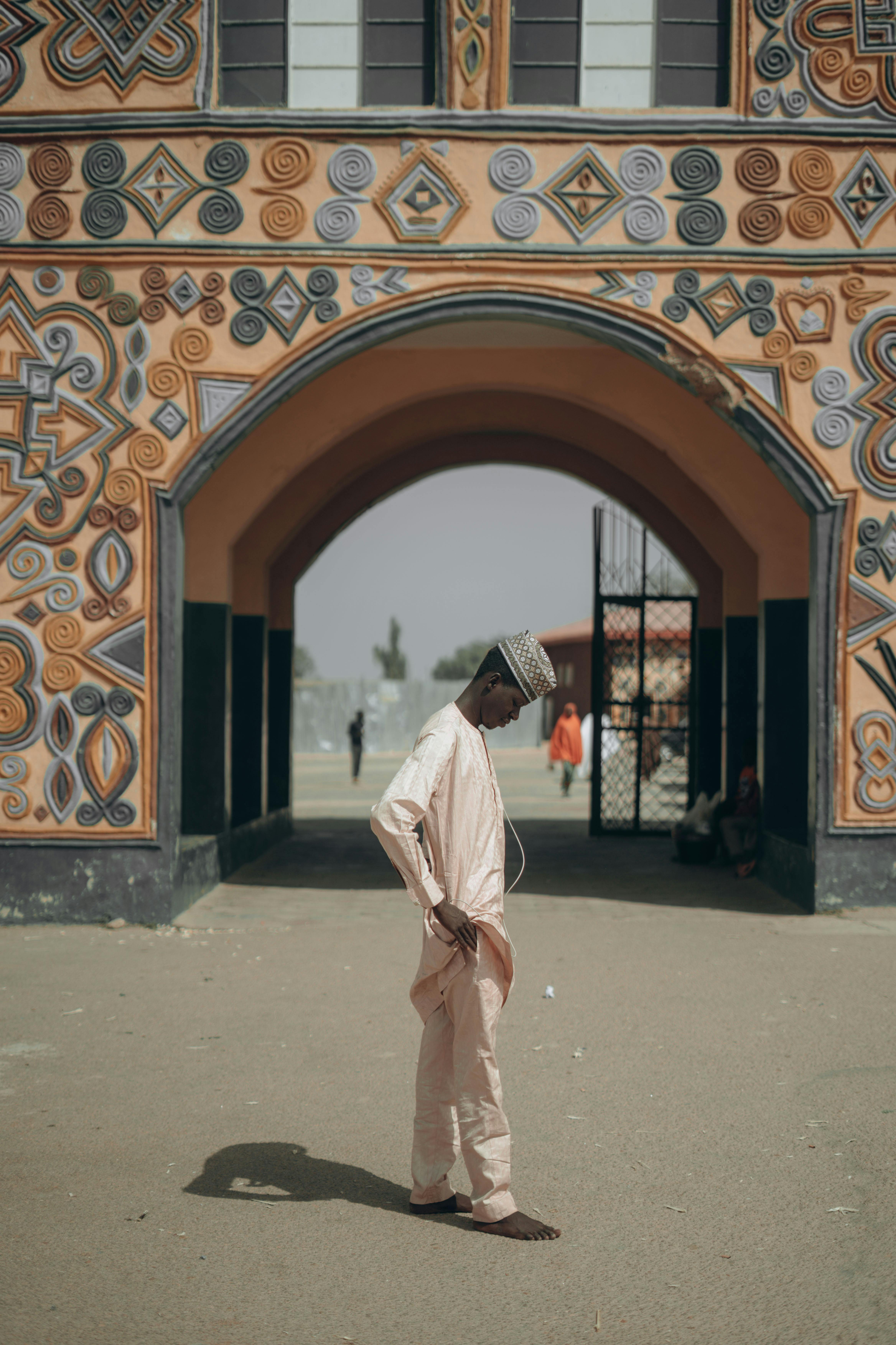 Man in Traditional Attire by Ornate African Archway · Free Stock Photo