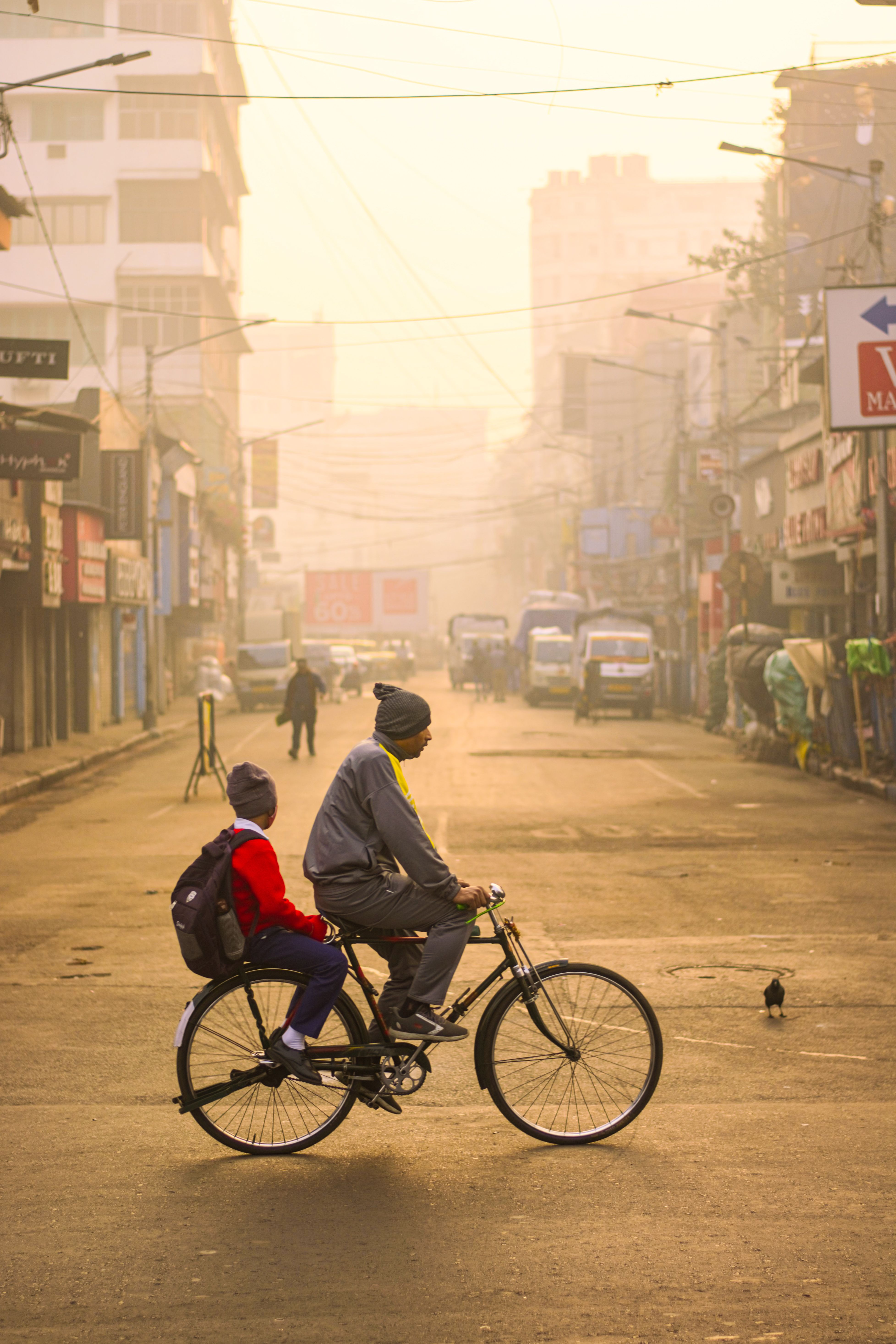 Father and child cycling on a city street at dawn · Free Stock Photo