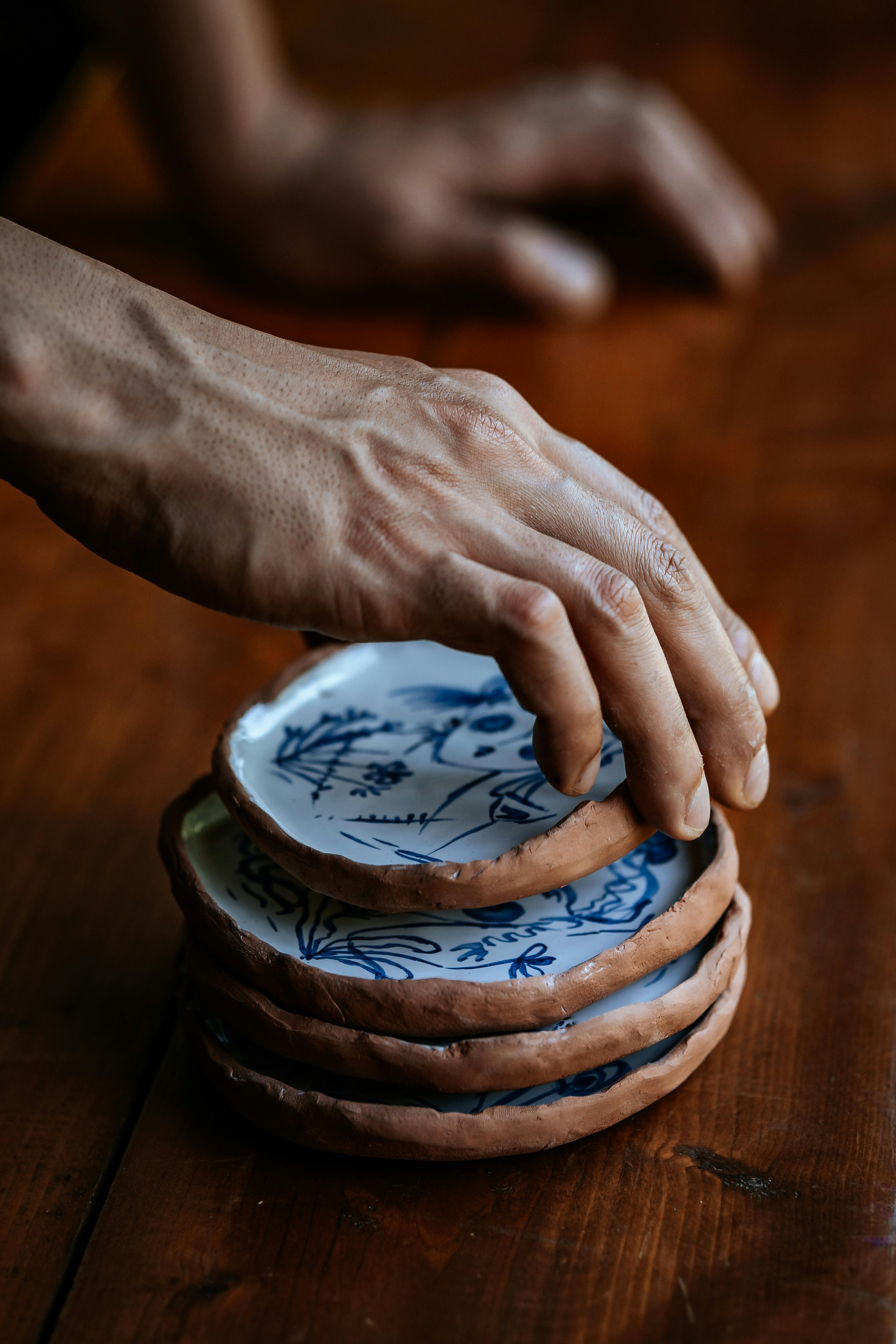 Hand Arranging Handmade Ceramic Plates on Wooden Table · Free Stock Photo