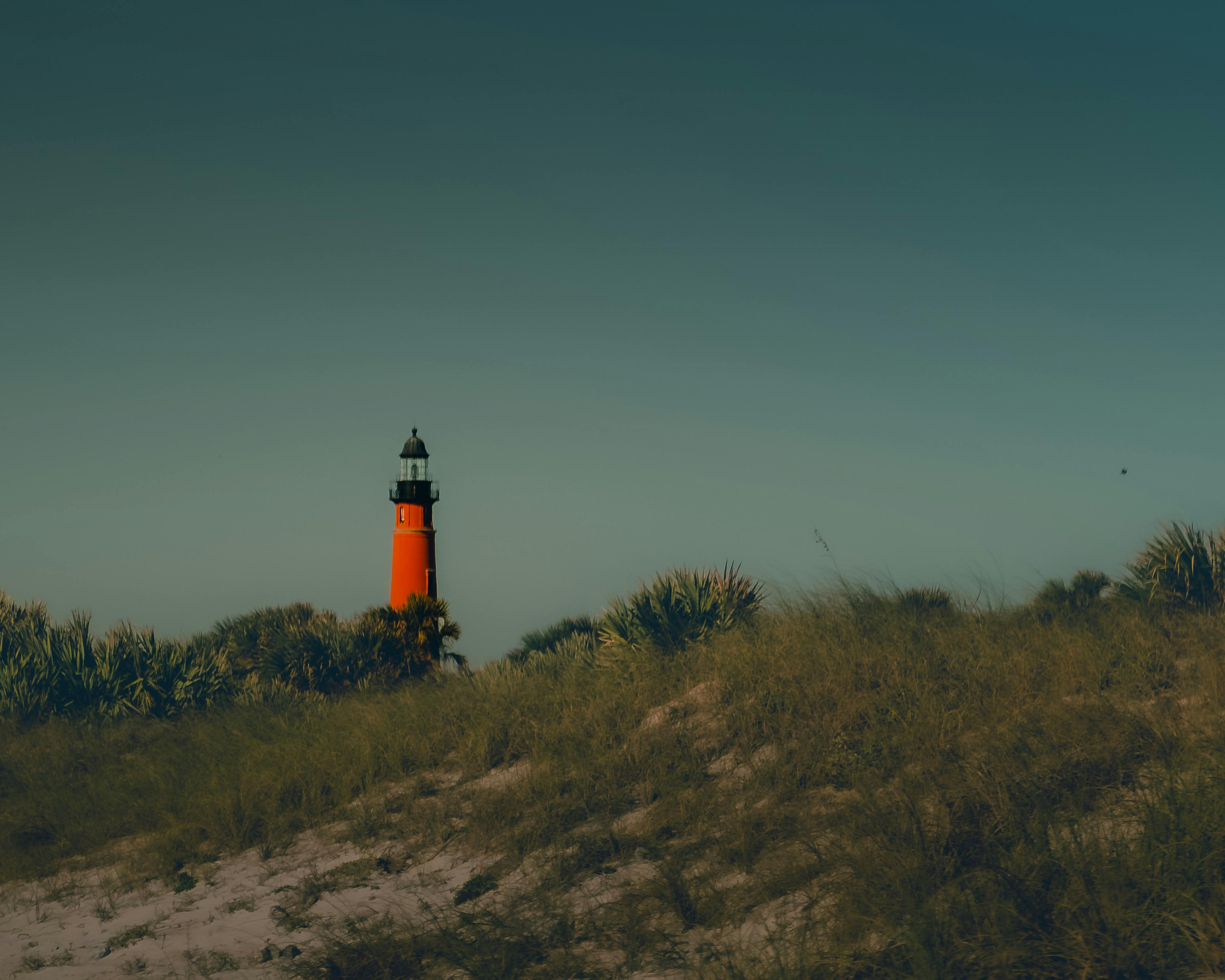 Orange Lighthouse Amid Coastal Dunes at Dusk · Free Stock Photo