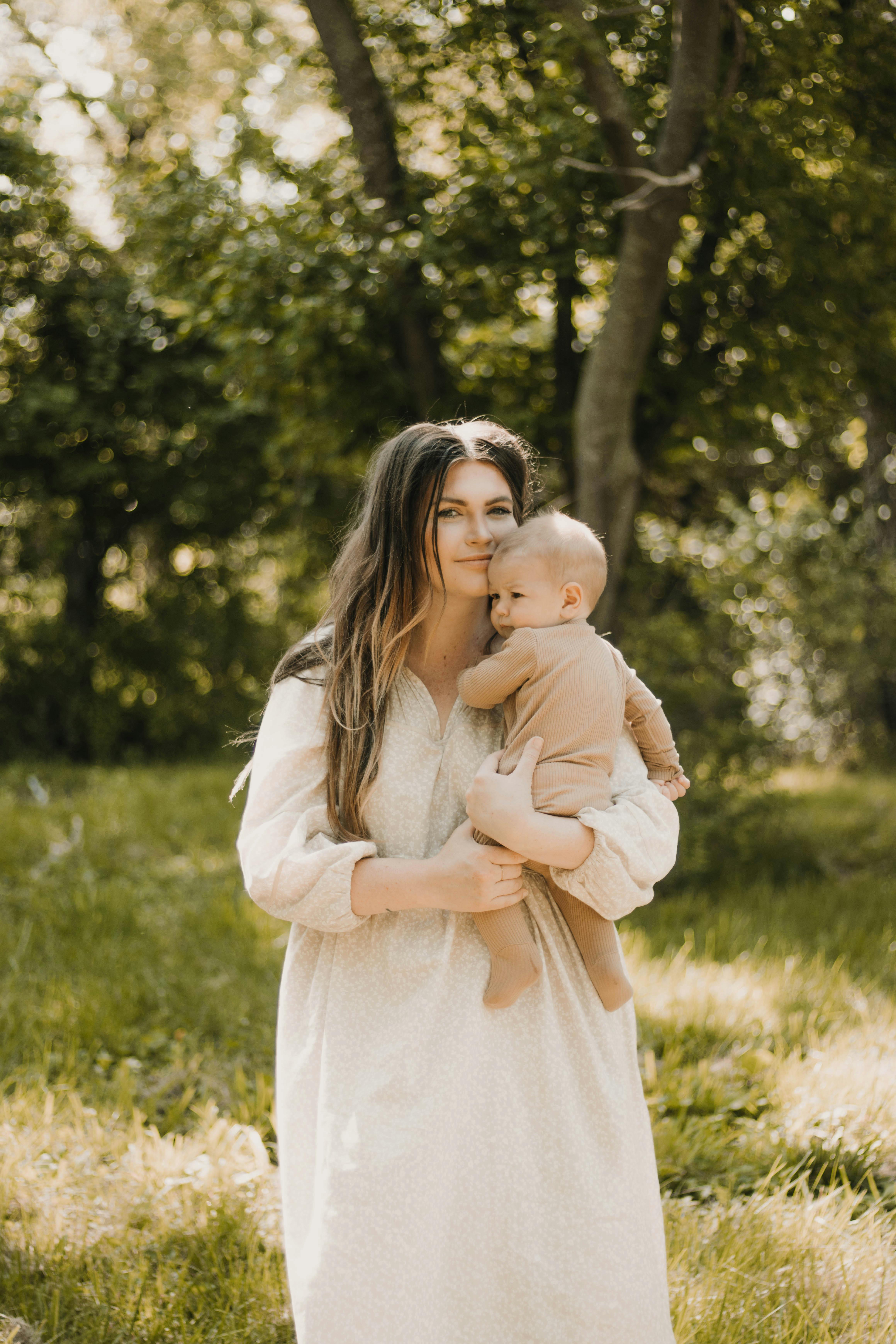 Mother Holding Baby in Sunny Woodland Setting · Free Stock Photo