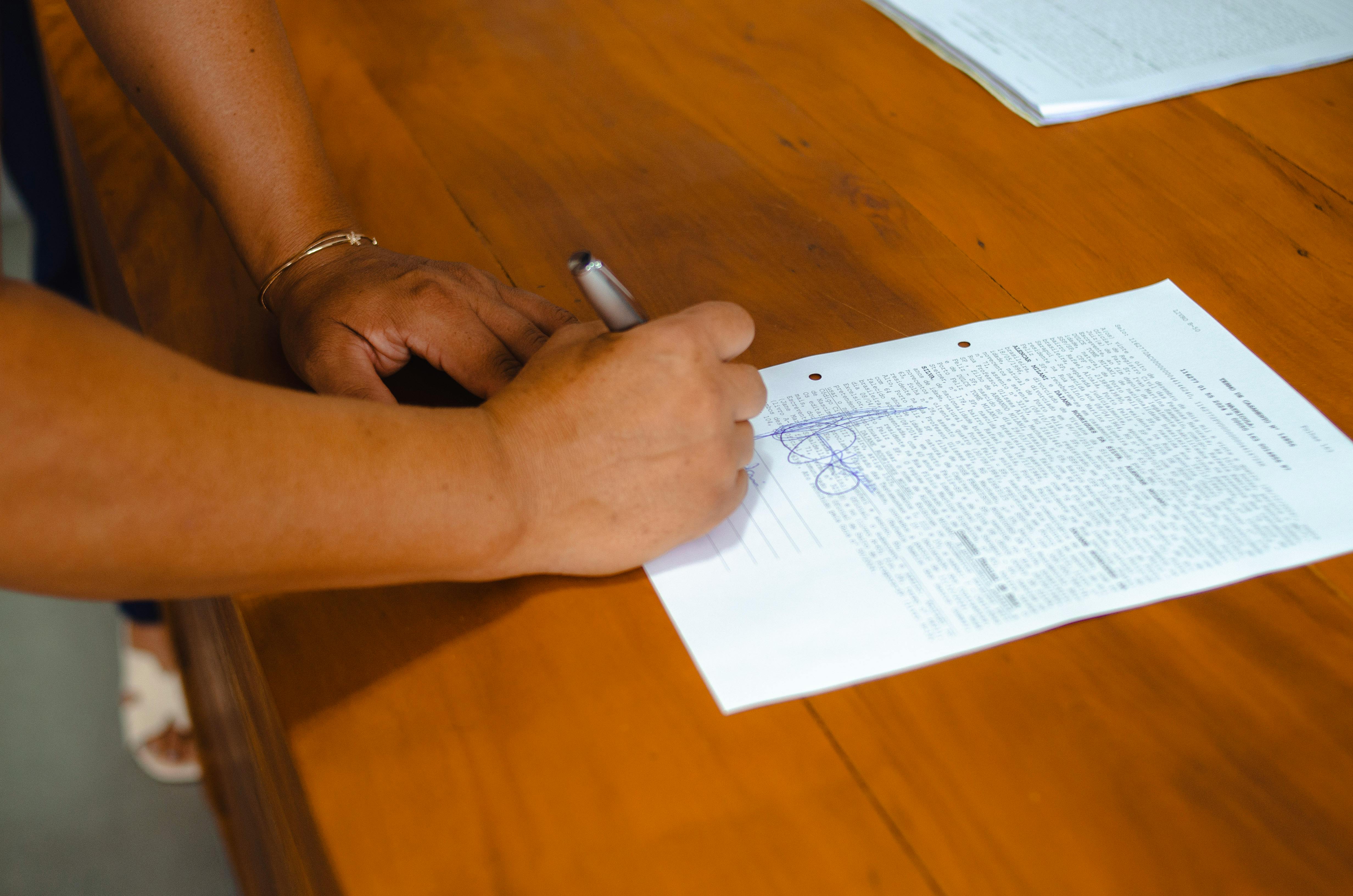 Person Signing Legal Document on Wooden Table · Free Stock Photo