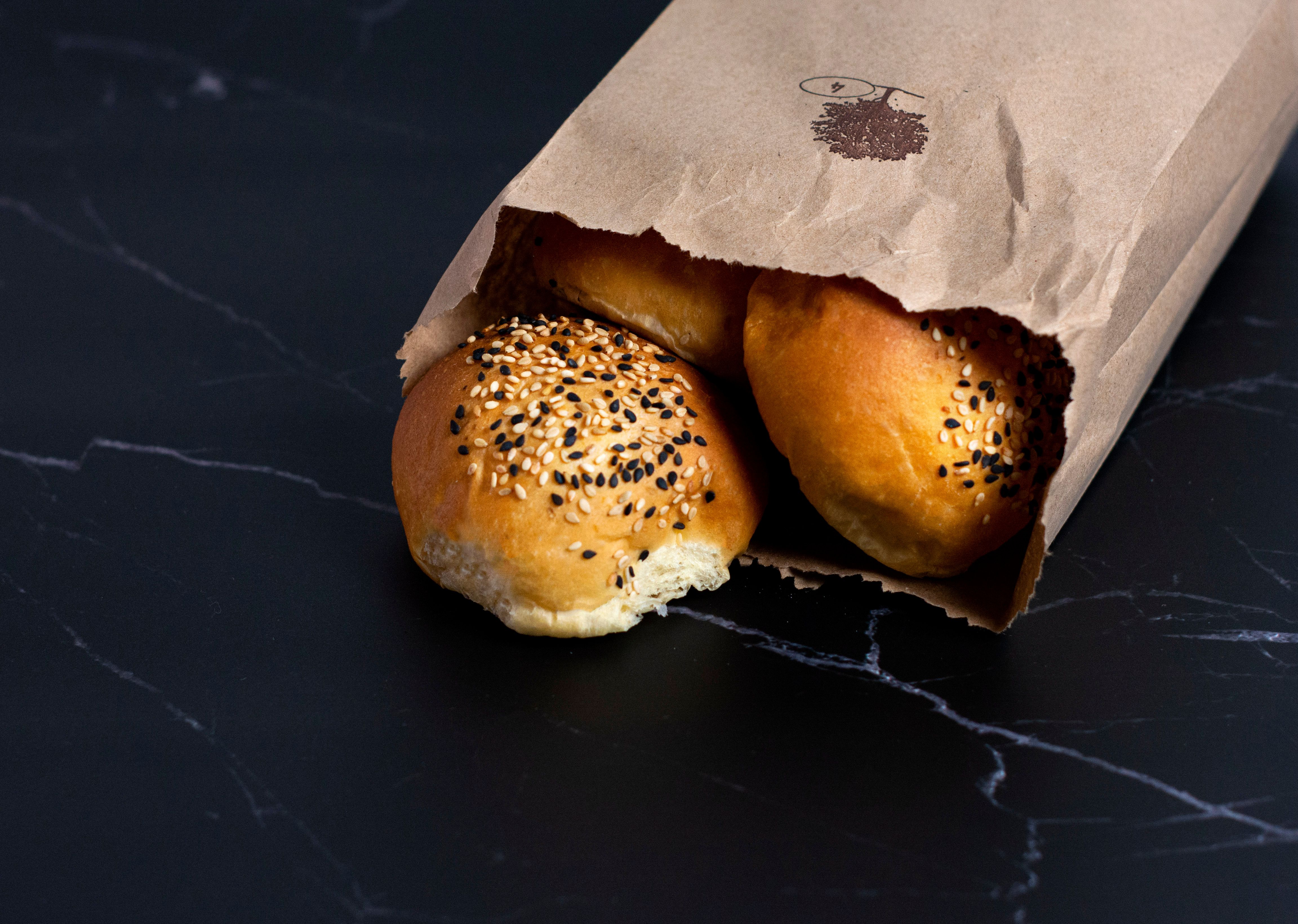 Fresh Artisan Bread in Paper Bag on Black Surface · Free Stock Photo