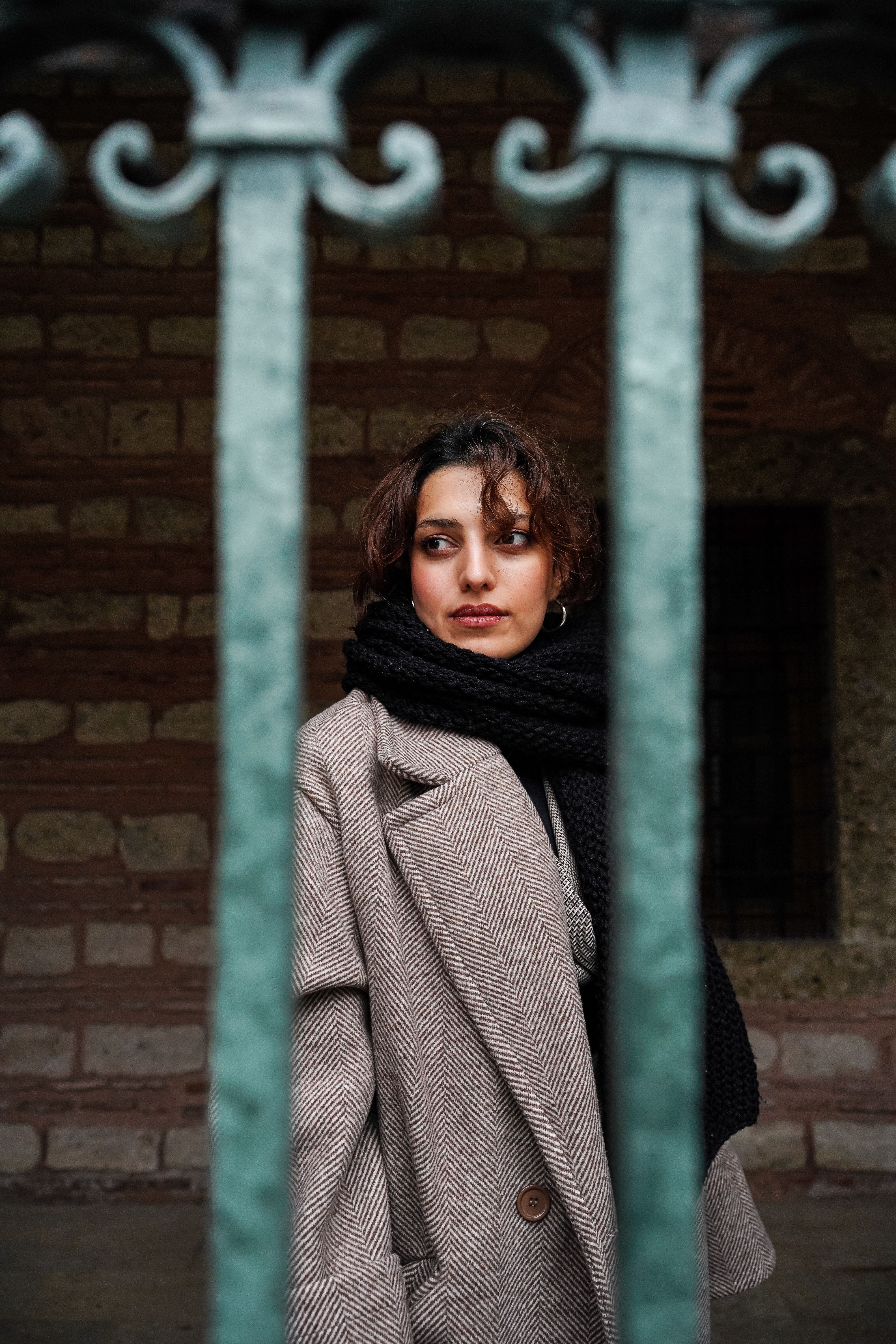 Free Woman stands pensively behind bars wearing a coat and scarf ...