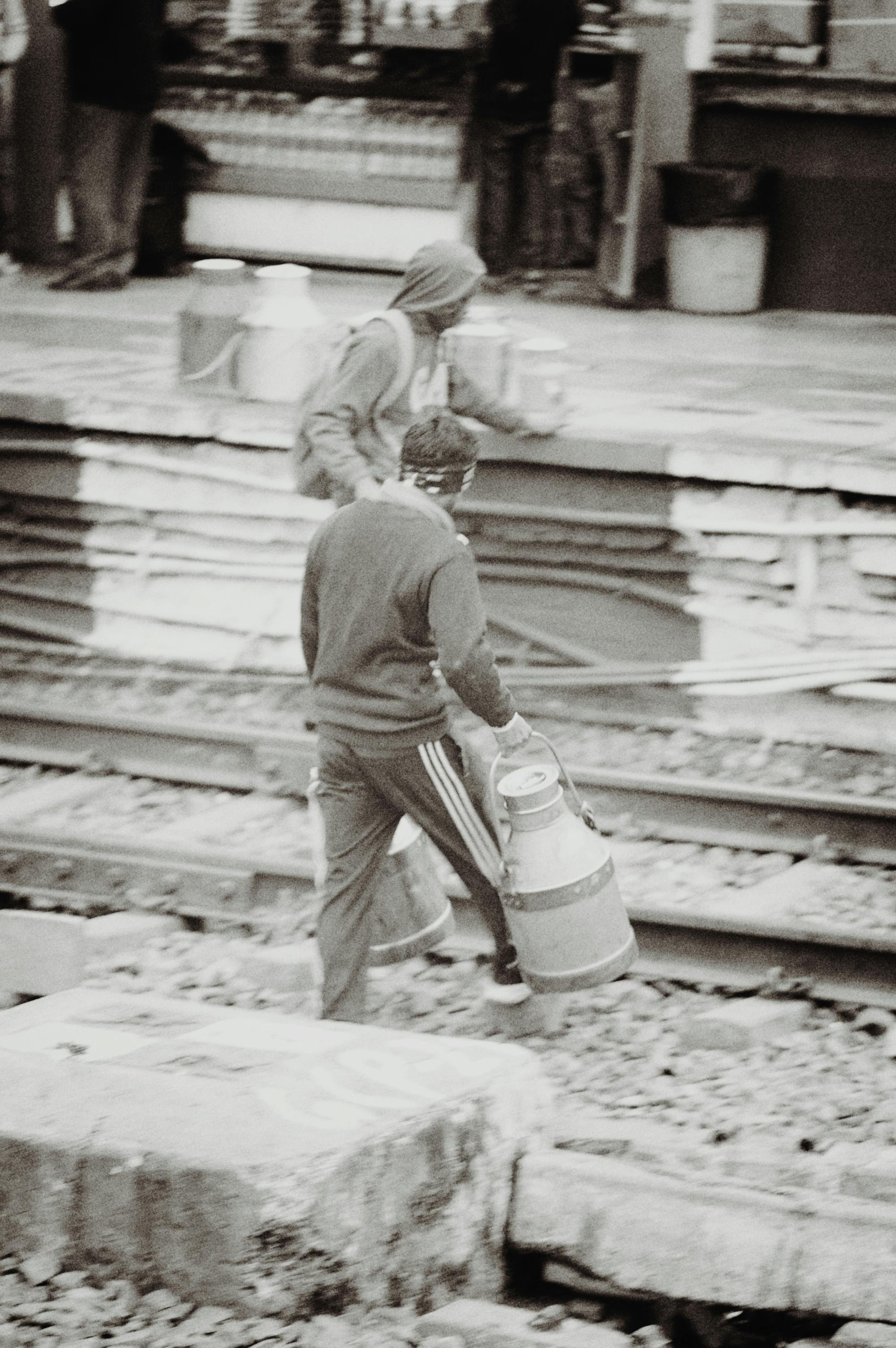 Men Carrying Milk Cans Across Train Tracks · Free Stock Photo