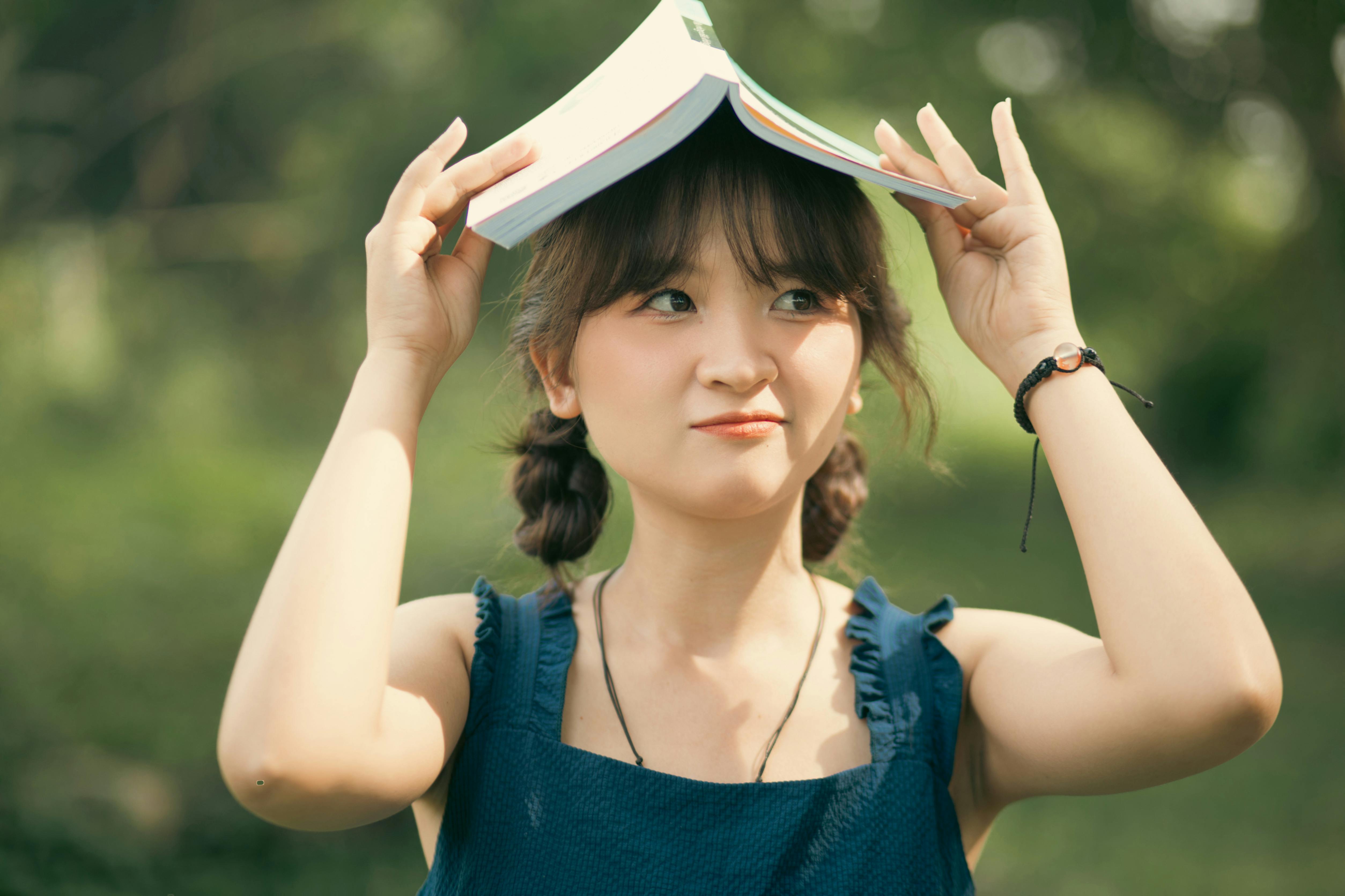 Young Woman Outdoors with Book on Head · Free Stock Photo