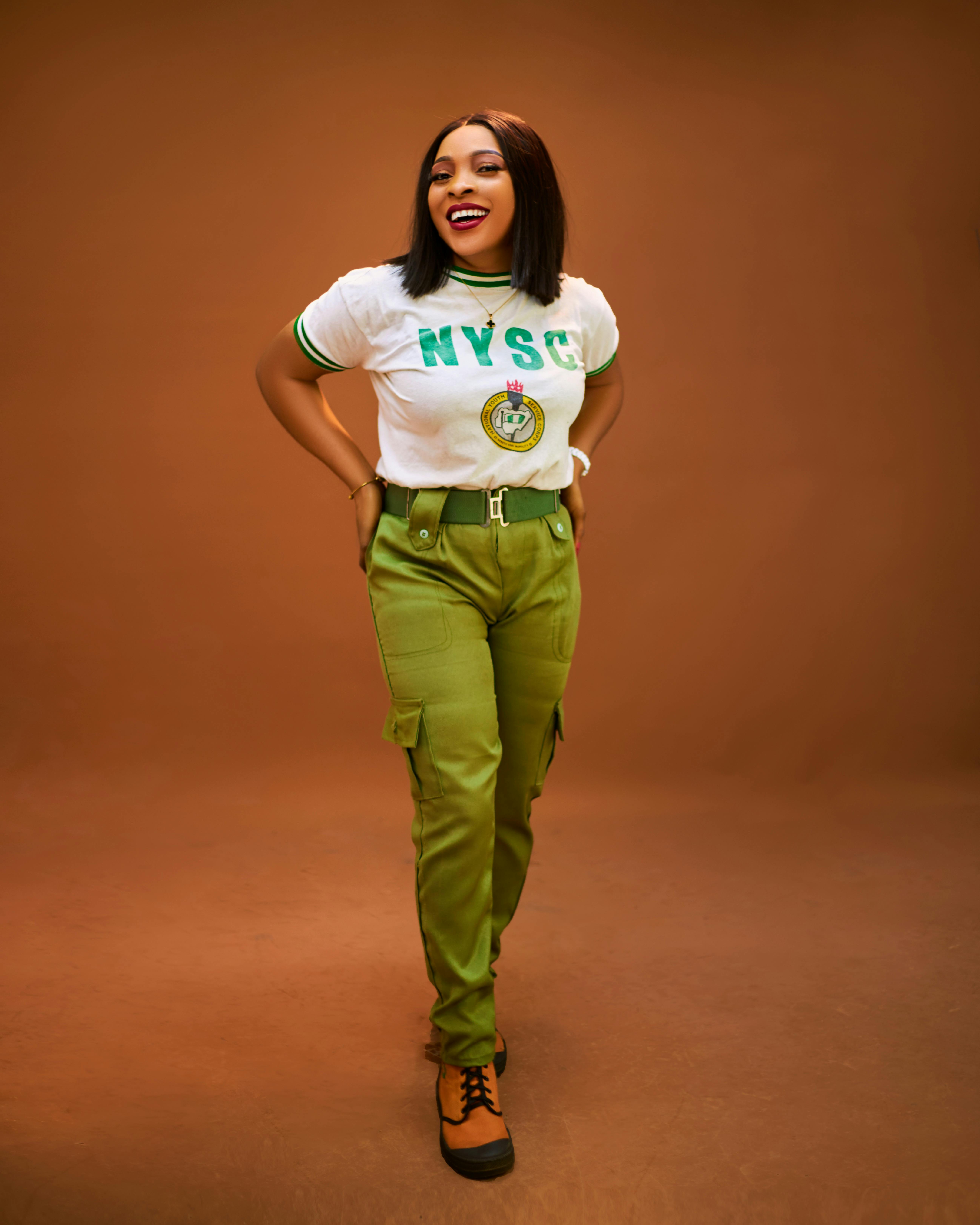 Smiling Woman in NYSC Uniform on Brown Background · Free Stock Photo