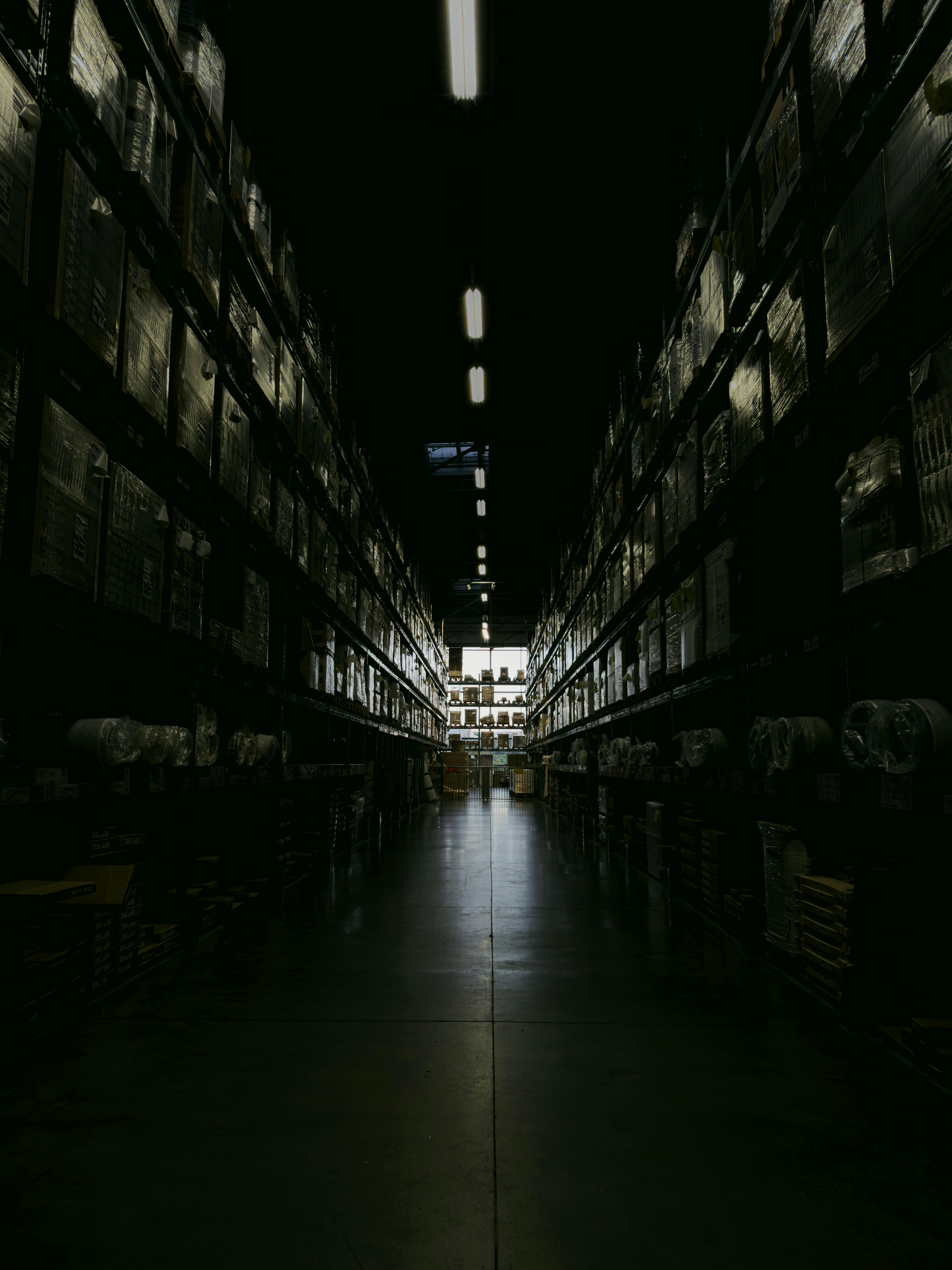 Dimly Lit Warehouse Aisle with Tall Shelves · Free Stock Photo