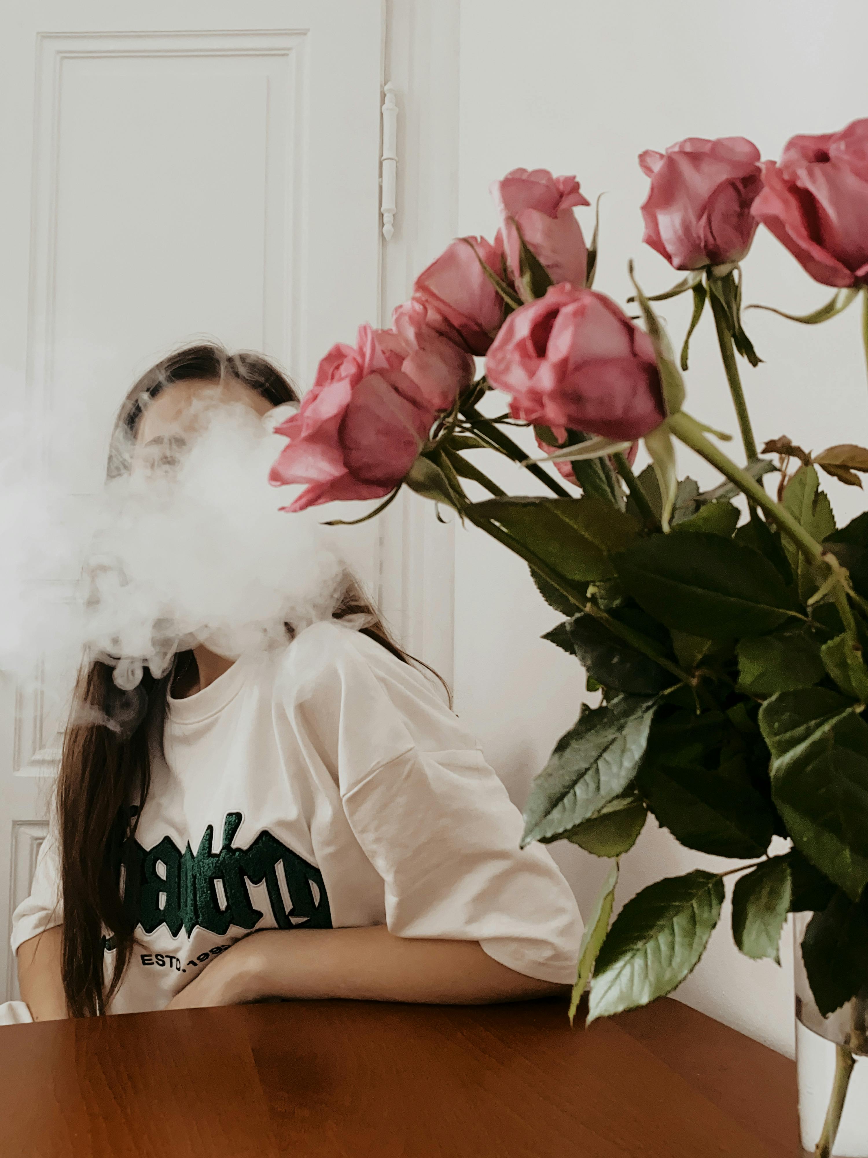 Woman vaping near vibrant pink roses indoors · Free Stock Photo