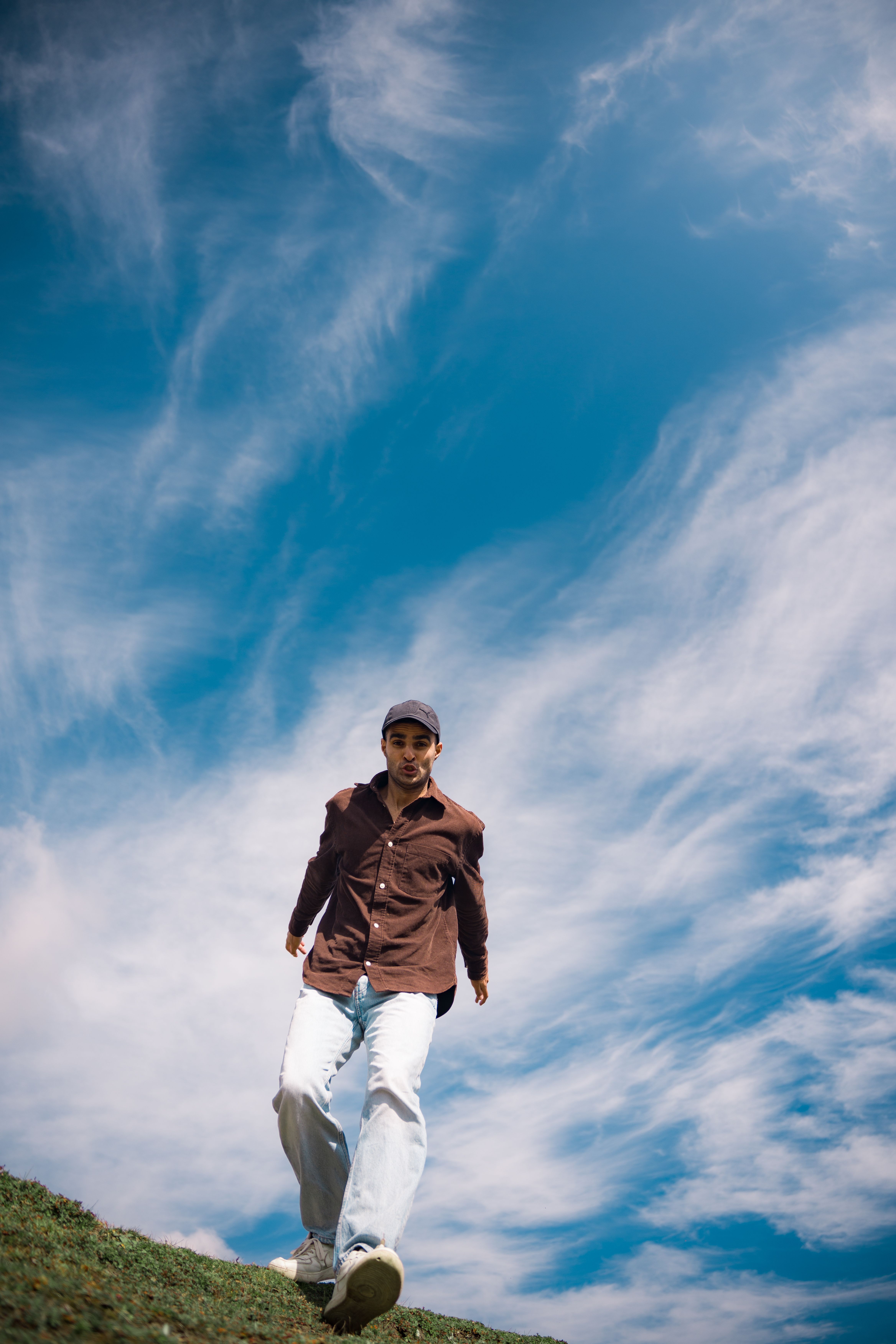 Man Walking Under Vibrant Blue Sky with Clouds · Free Stock Photo