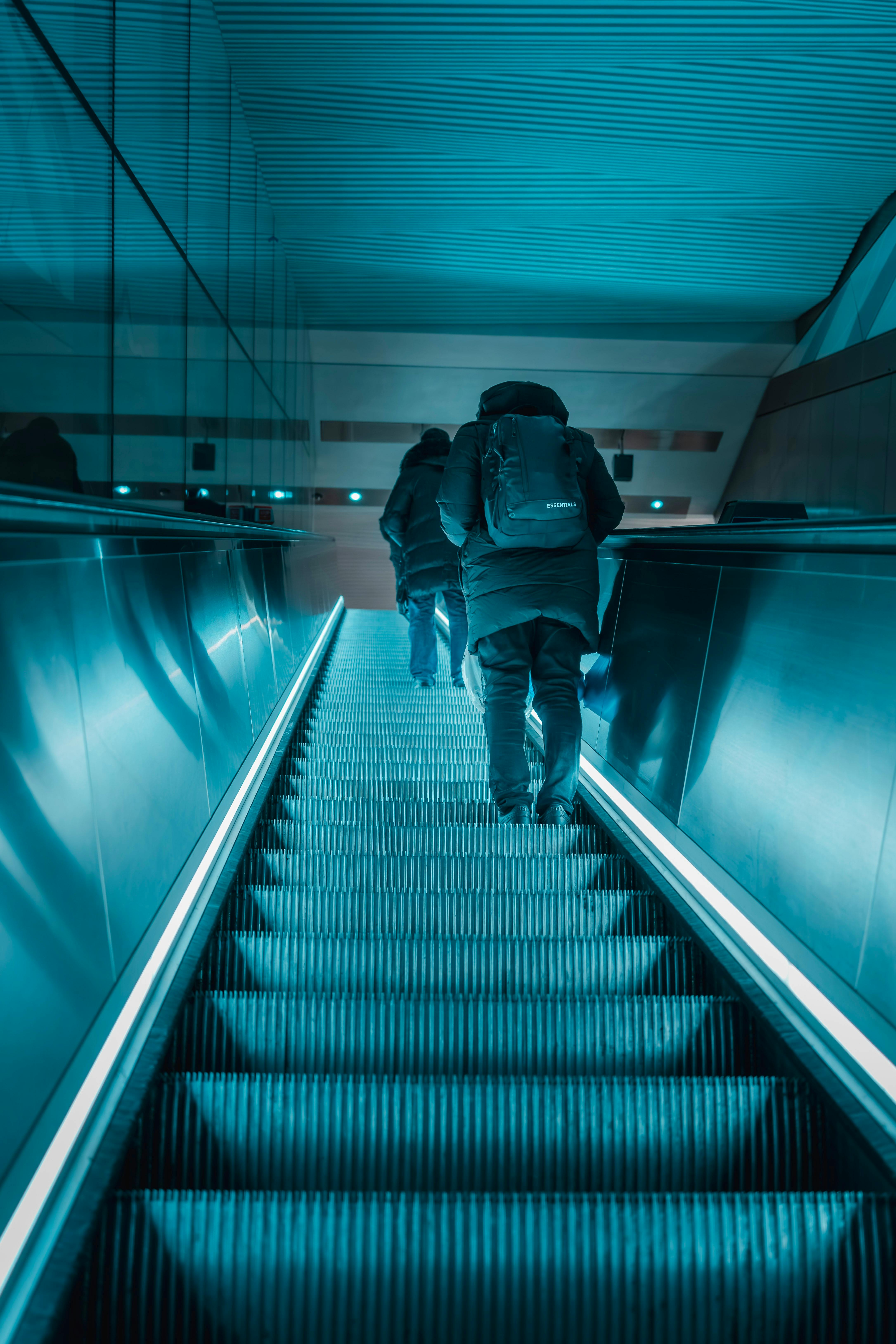 Two People on Illuminated Blue Escalator · Free Stock Photo