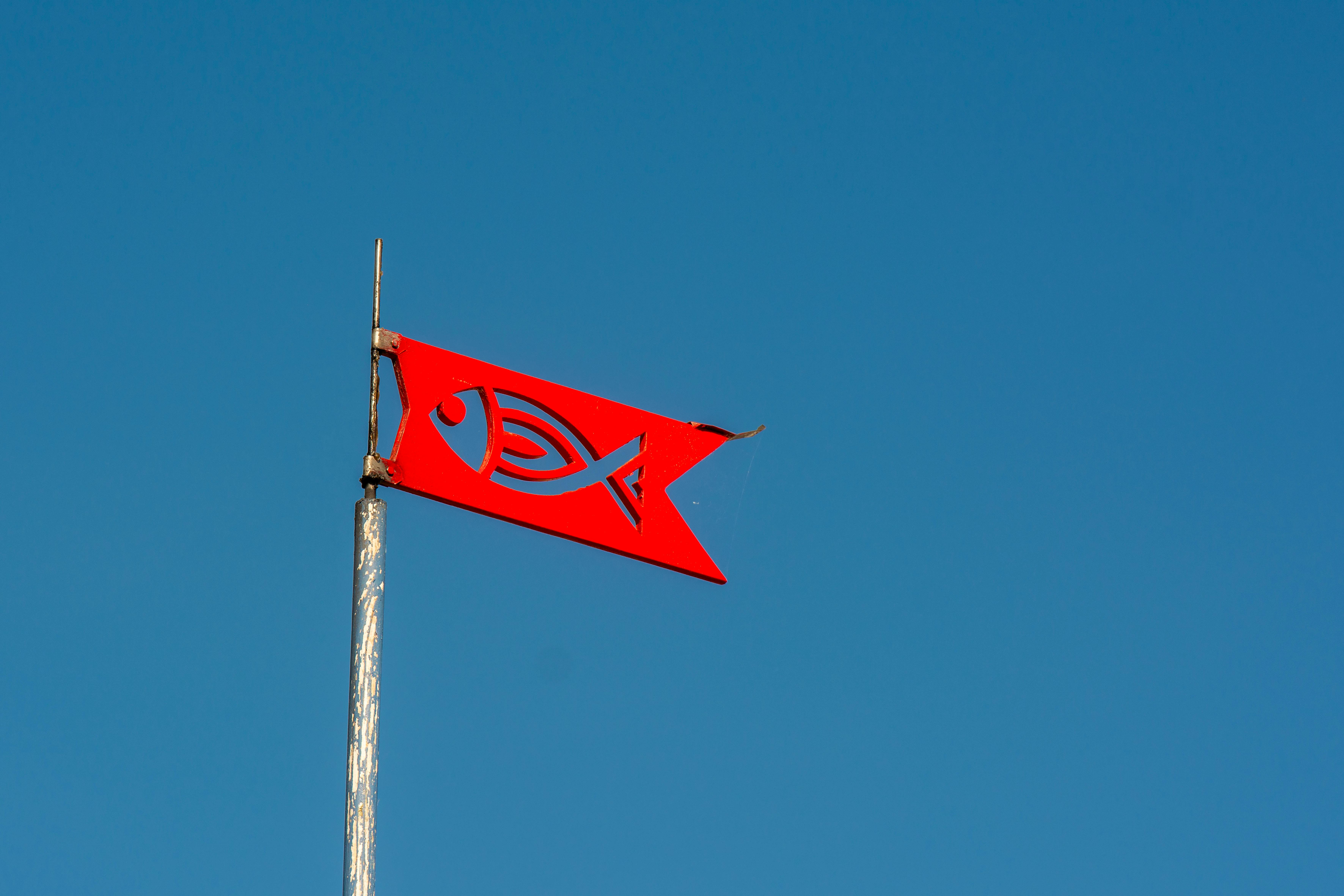Red Flag with Fish Symbol Against Clear Blue Sky · Free Stock Photo
