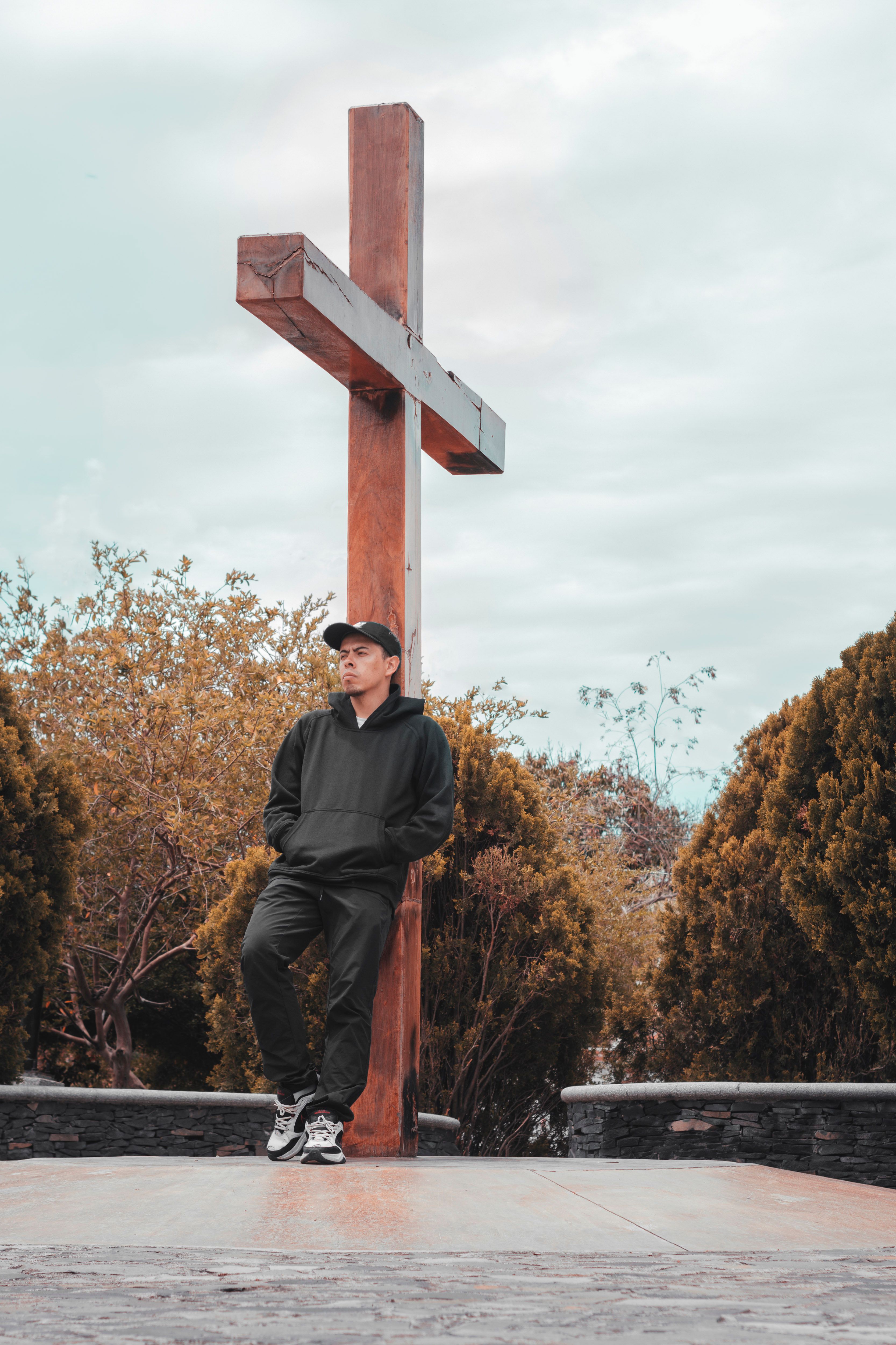 Man Leaning on Large Cross in Outdoor Setting · Free Stock Photo