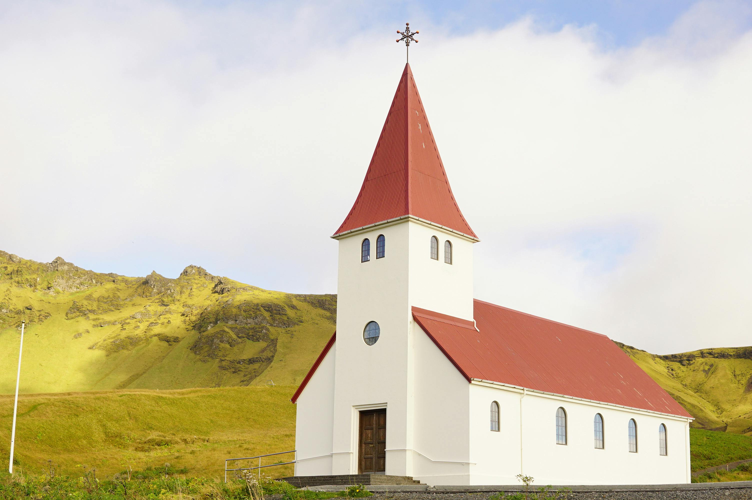 A picturesque church with a red roof against a lush green Icelandic hill under a clear sky.