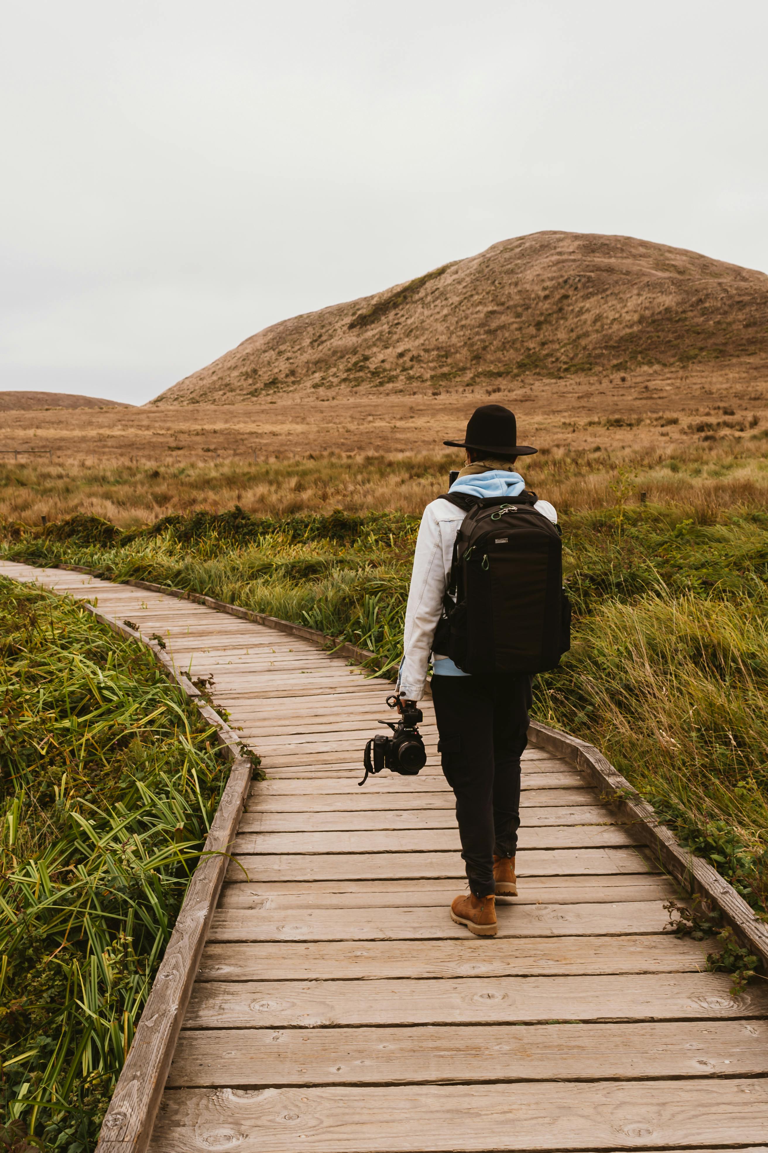 Man Walking on Wooden Pathway Surrounded By Grassland · Free Stock Photo