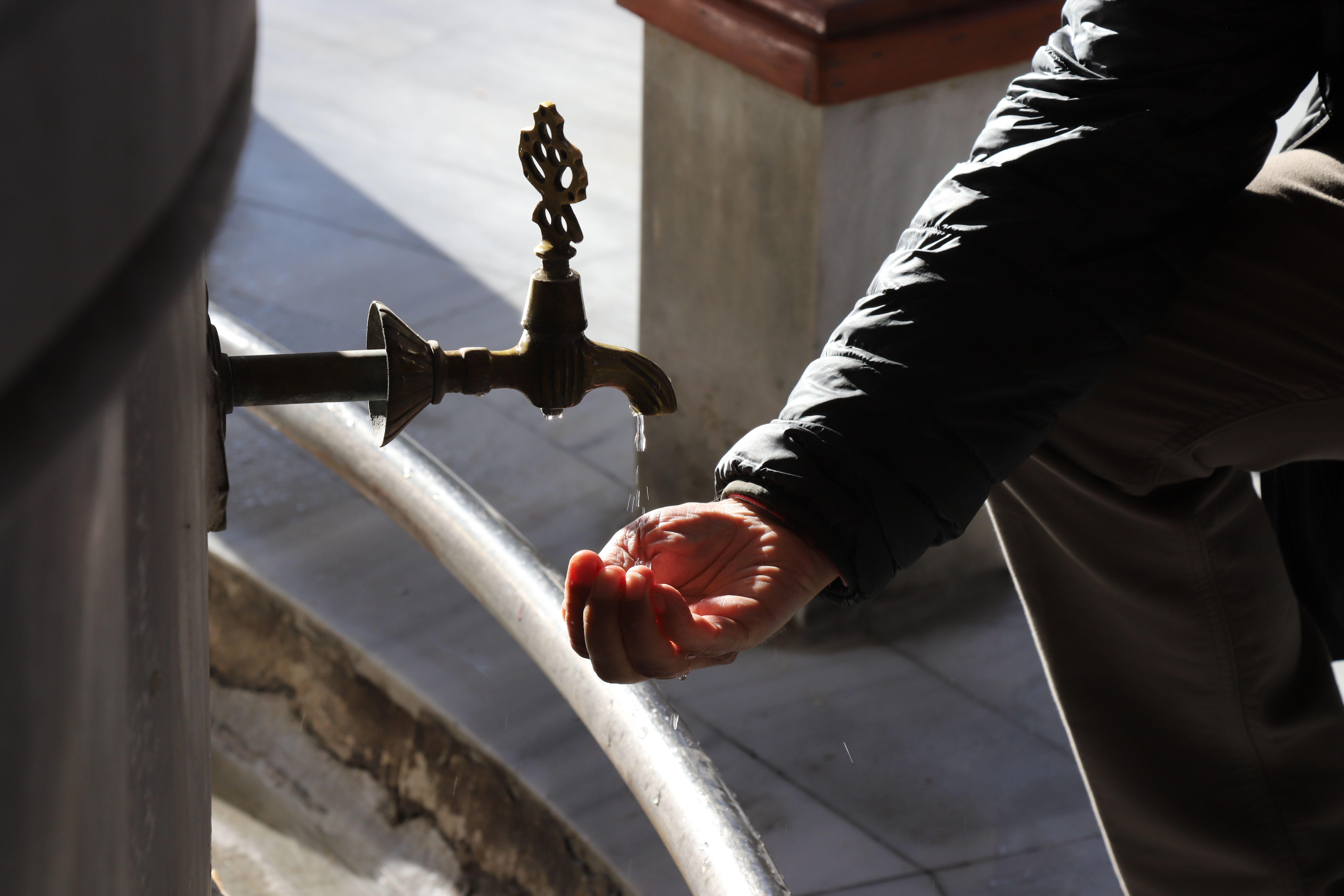 Hand receiving water from an ornate outdoor tap · Free Stock Photo