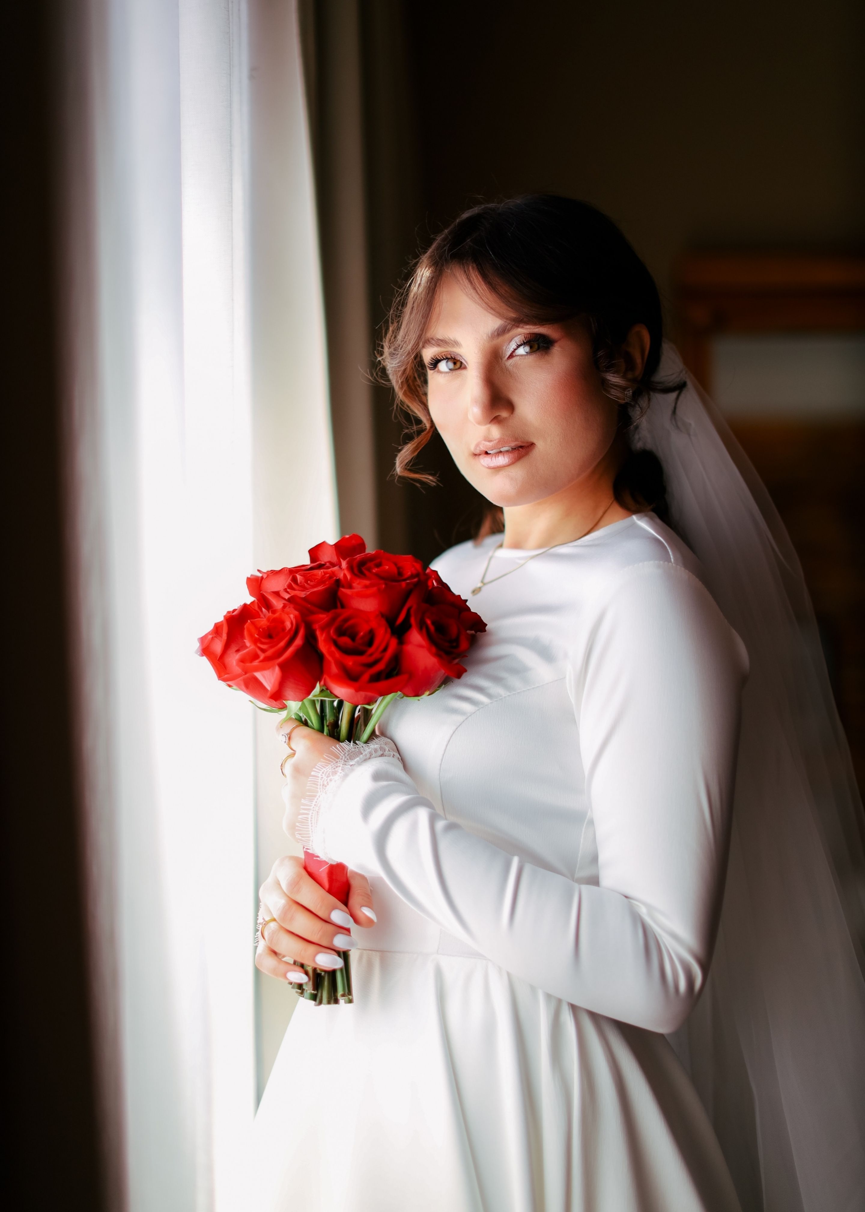 Mariée élégante Tenant Des Roses Rouges Près D'une Fenêtre · Photo gratuite