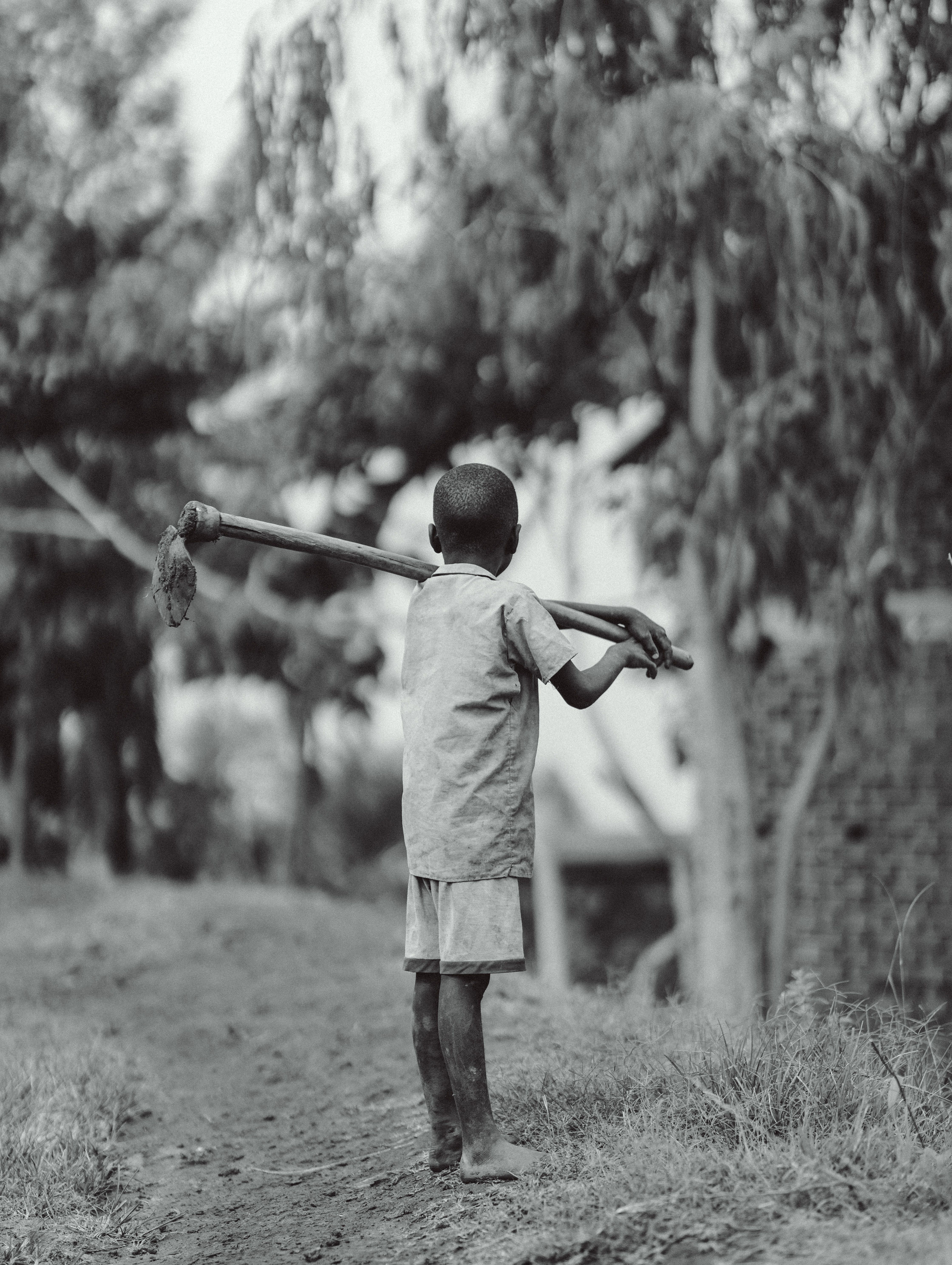 Child Farmer Holding Hoe in Rural Landscape · Free Stock Photo