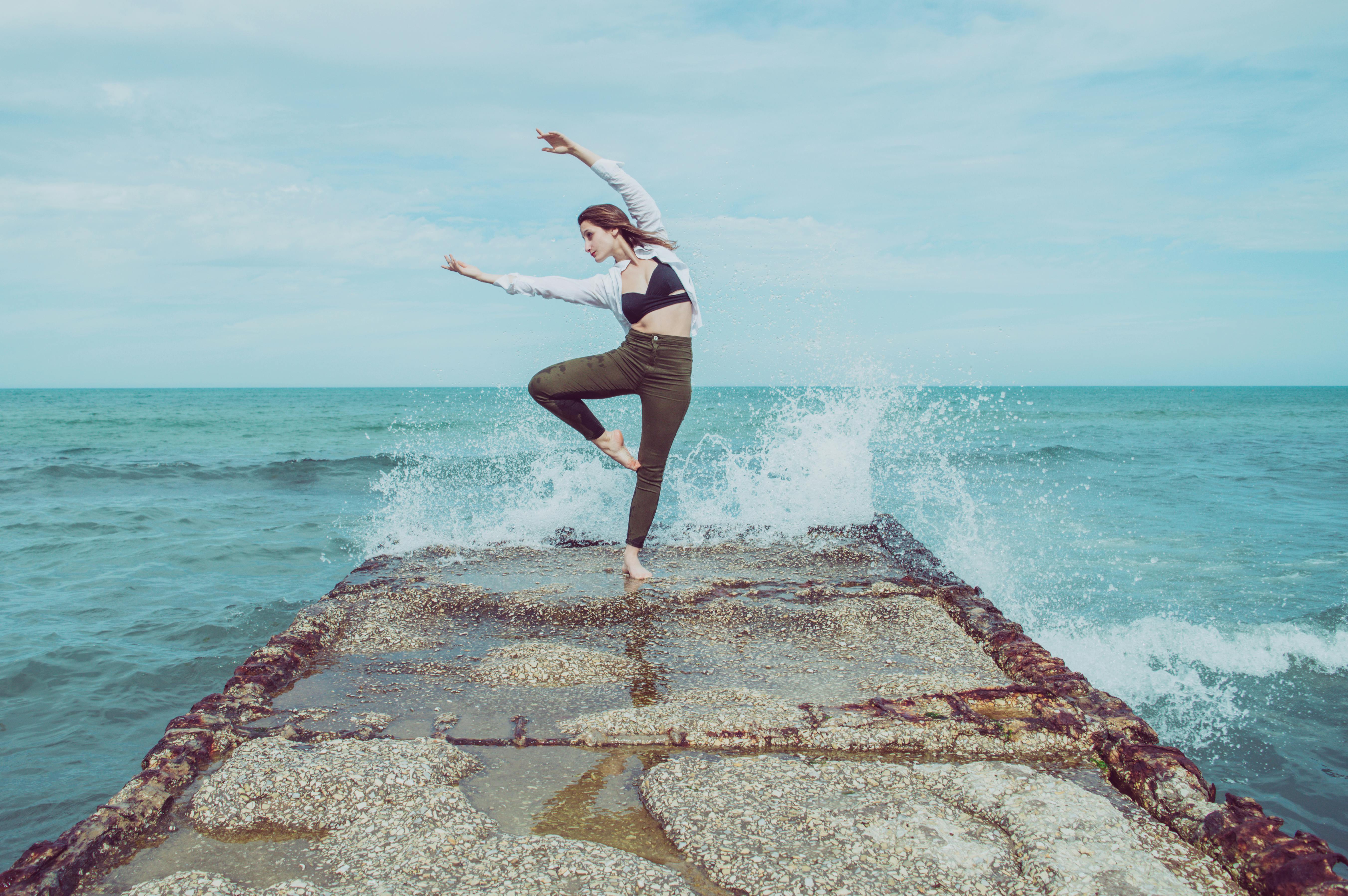 Woman Doing Ballet Pose On The Breakwater With Waves Splashing Behind ...
