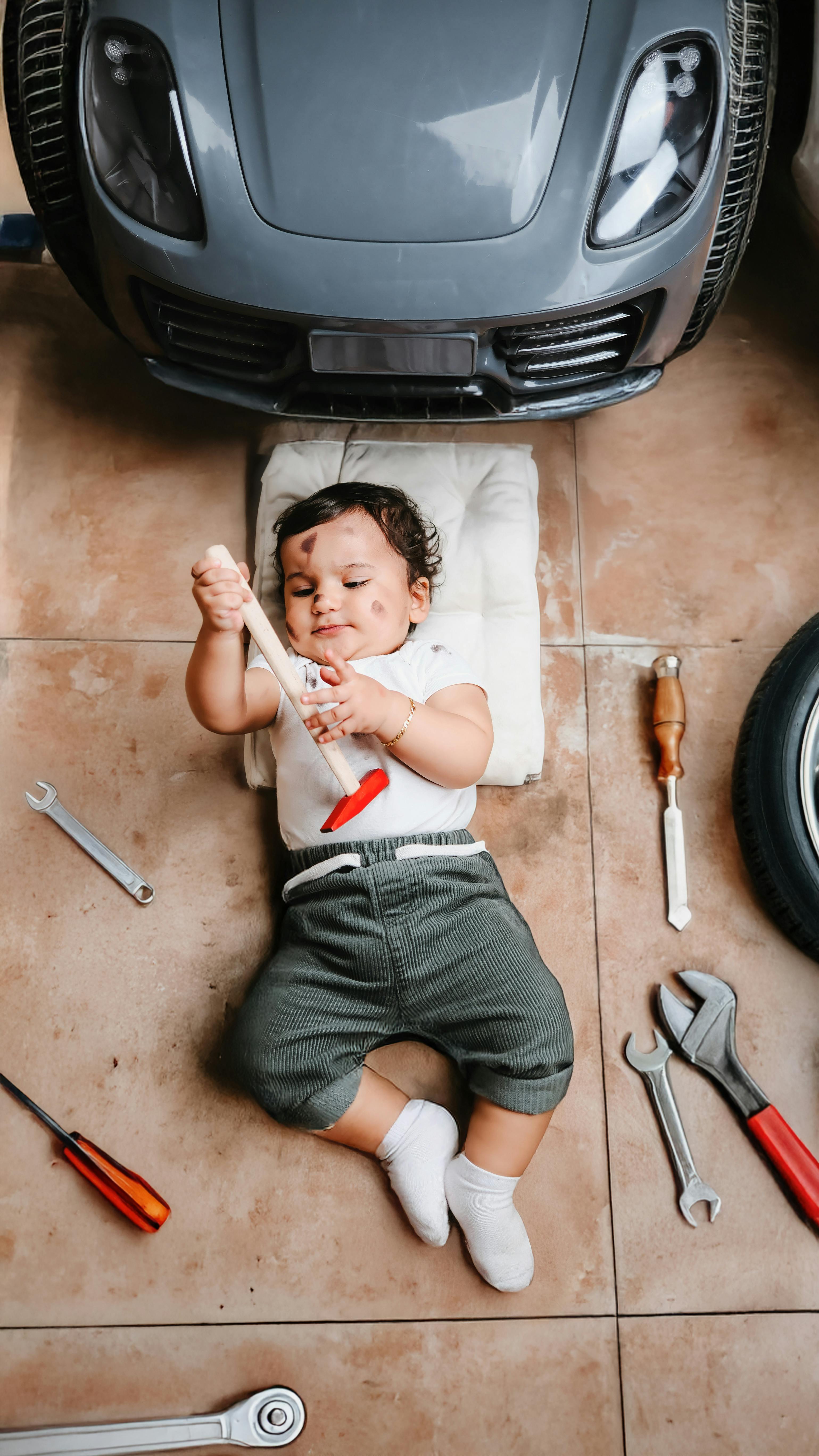 Cute baby mechanic with tools under car · Free Stock Photo