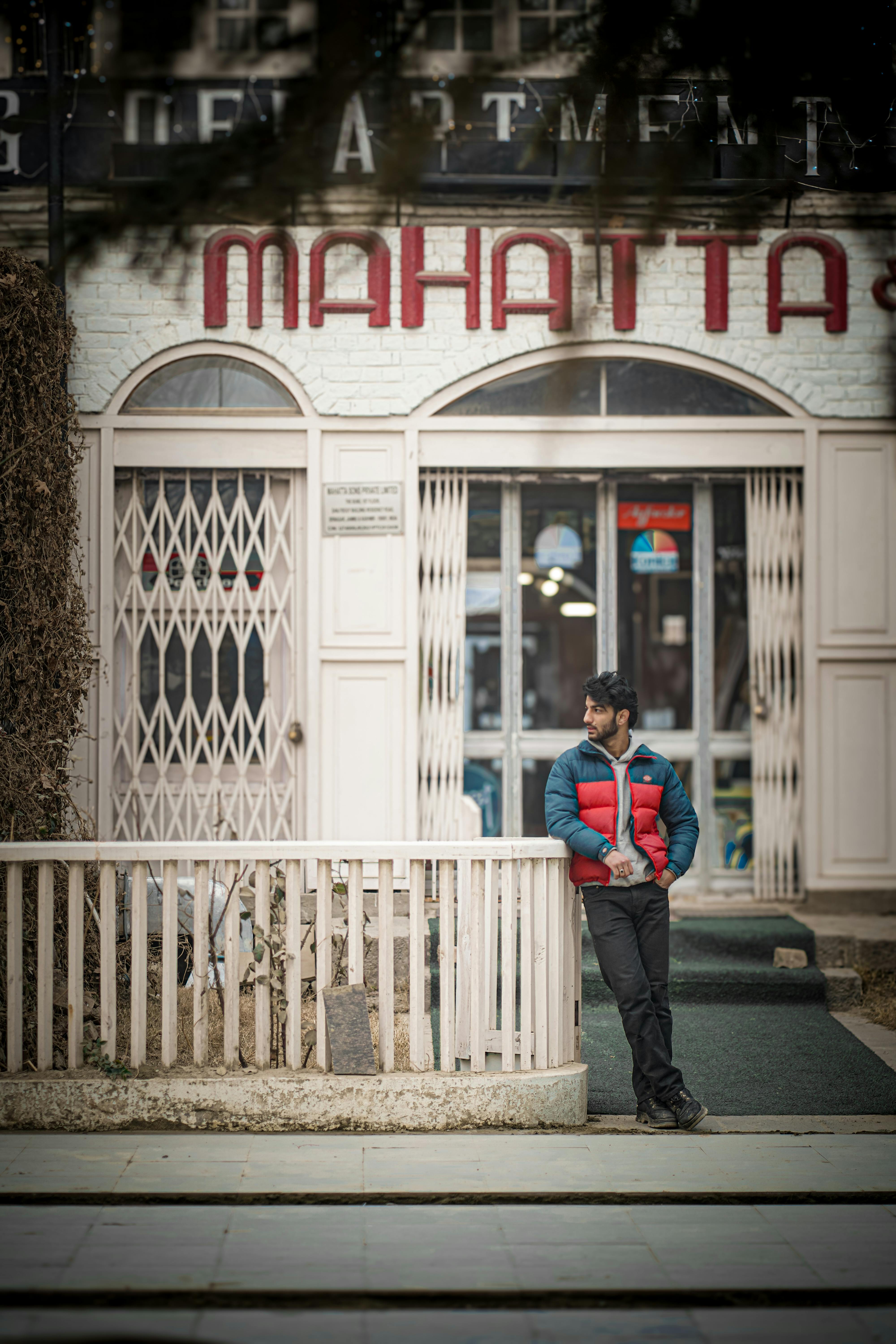Man Leaning Against Fence with Mahatta Sign · Free Stock Photo