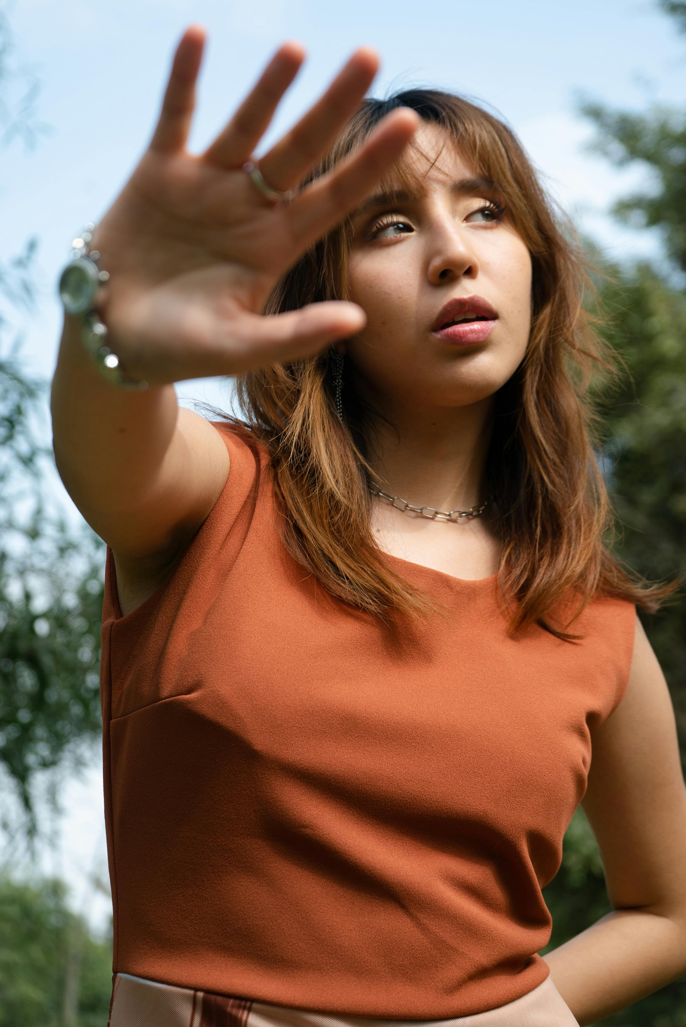 Young Woman Outdoors Blocking Camera with Hand · Free Stock Photo