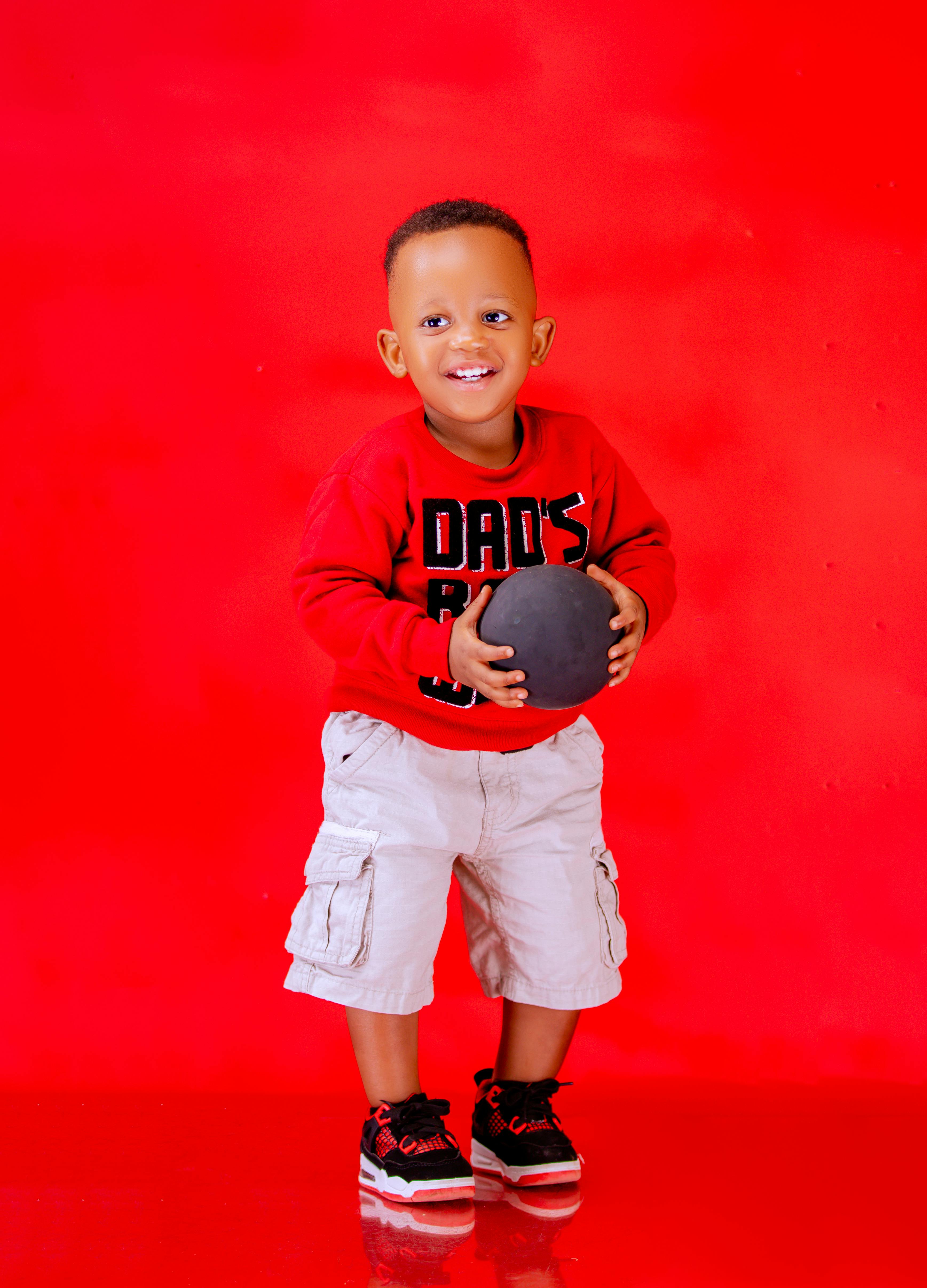Smiling Child Holding Ball on Red Background · Free Stock Photo
