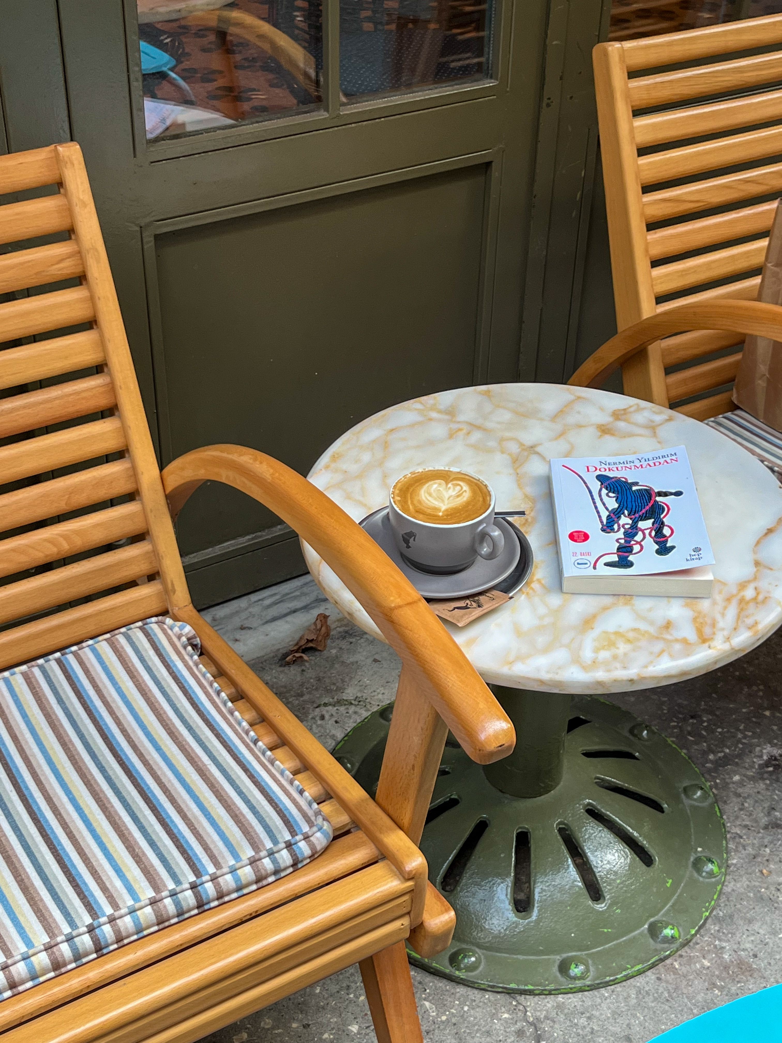Cozy outdoor cafe scene with coffee and book · Free Stock Photo