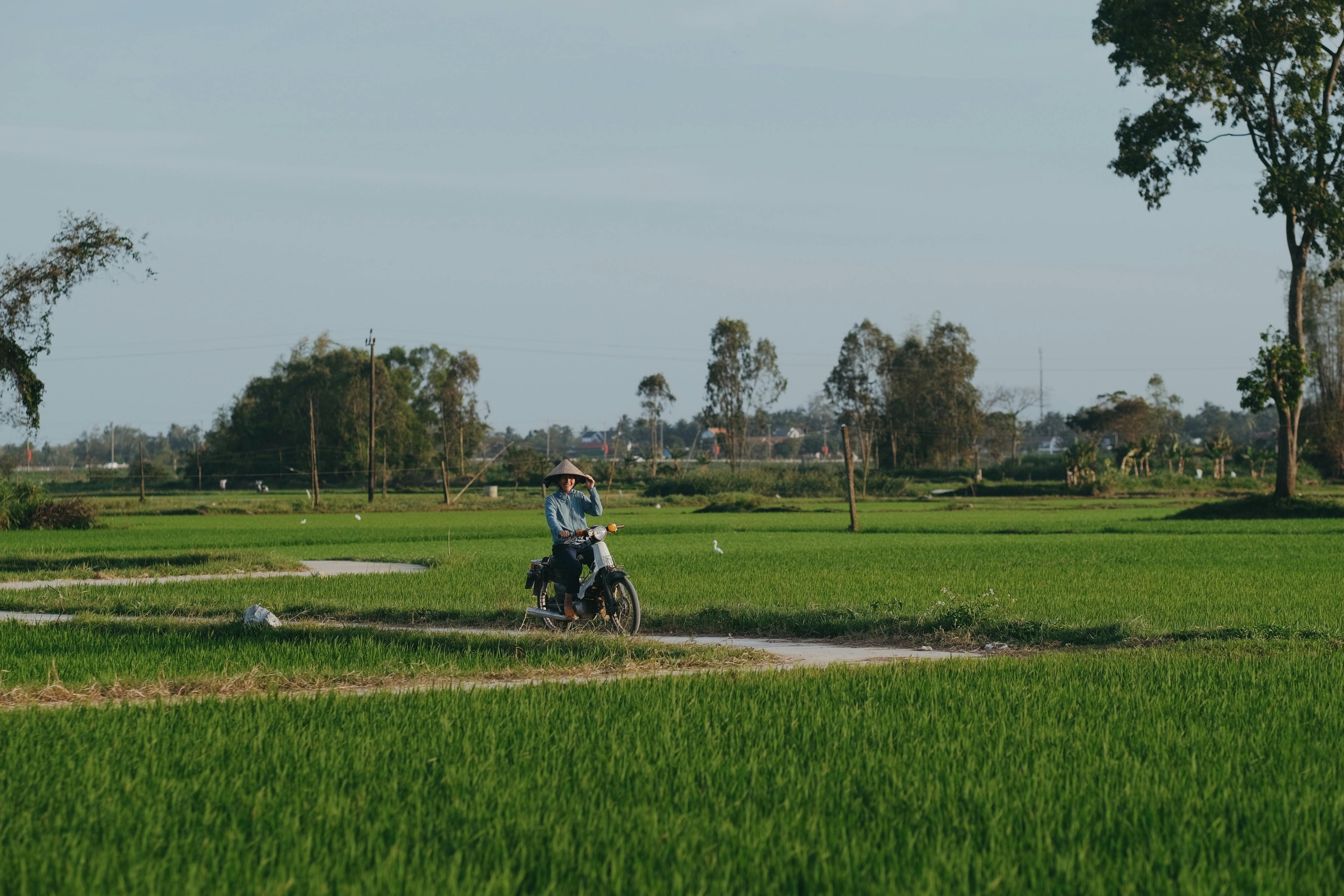 Rural Scene with Farmer Riding Motorcycle in Green Field · Free Stock Photo