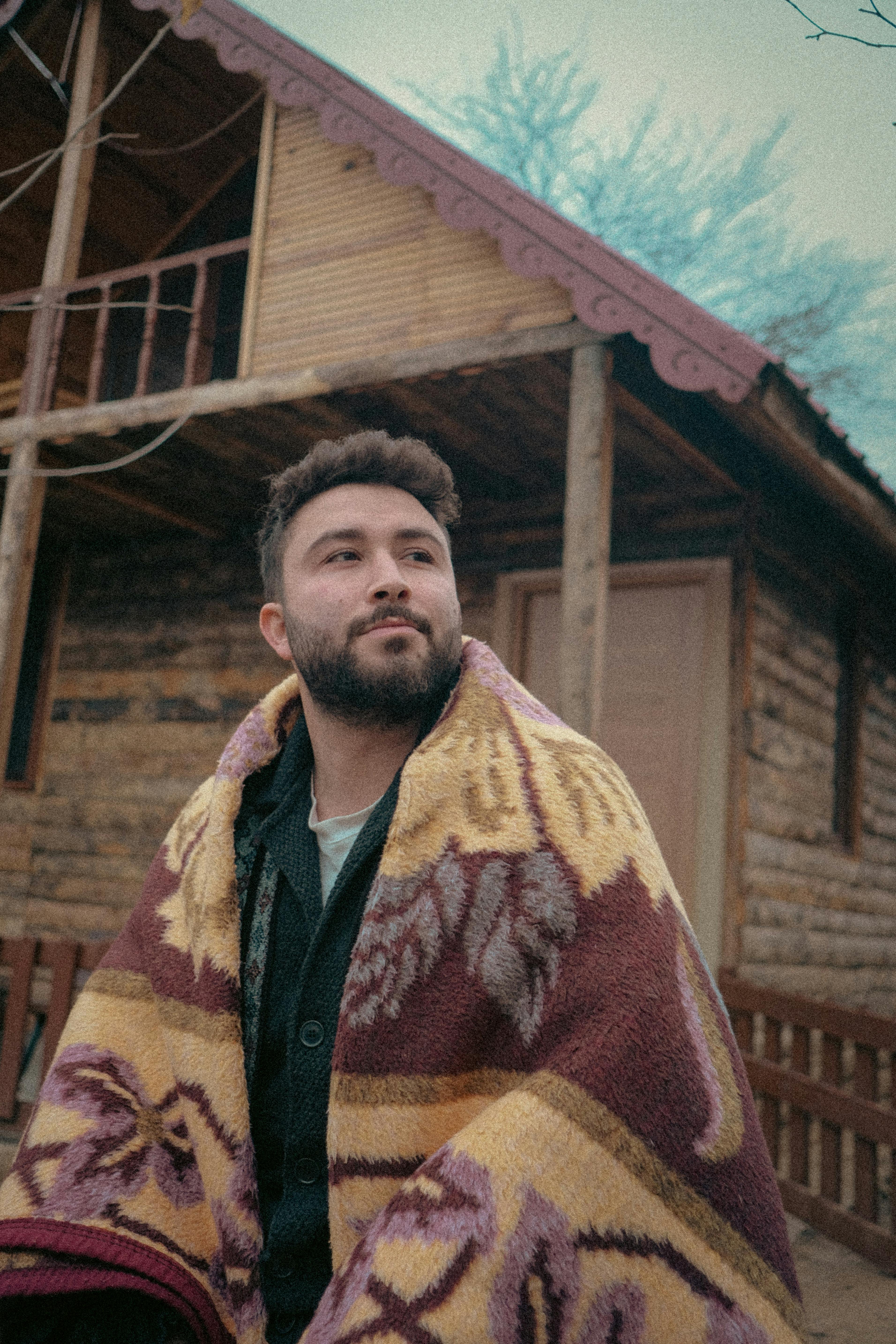Cozy Man Wrapped in Blanket Outside Rustic Cabin · Free Stock Photo