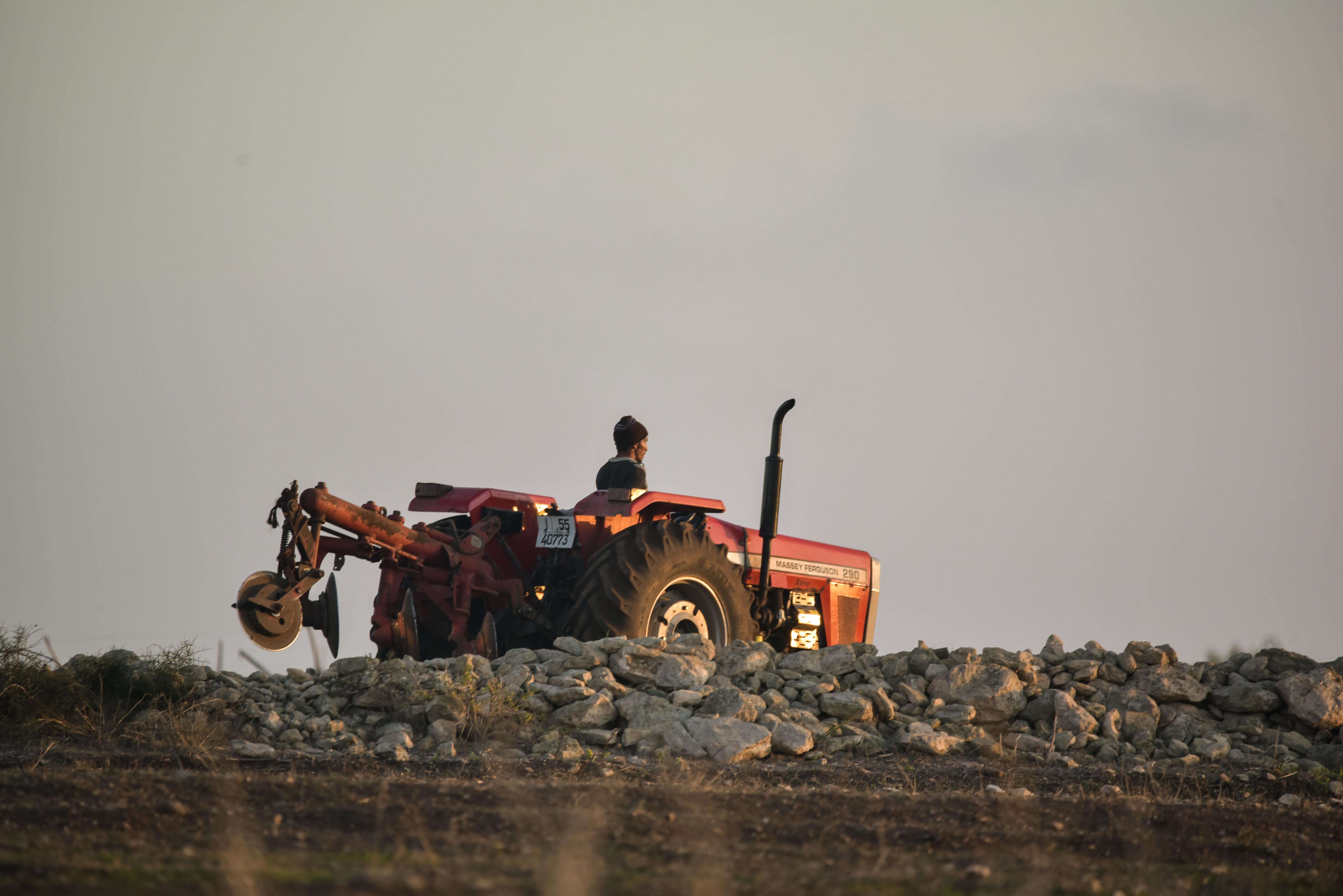 Farmer on Red Tractor in Rocky Field at Dawn · Free Stock Photo
