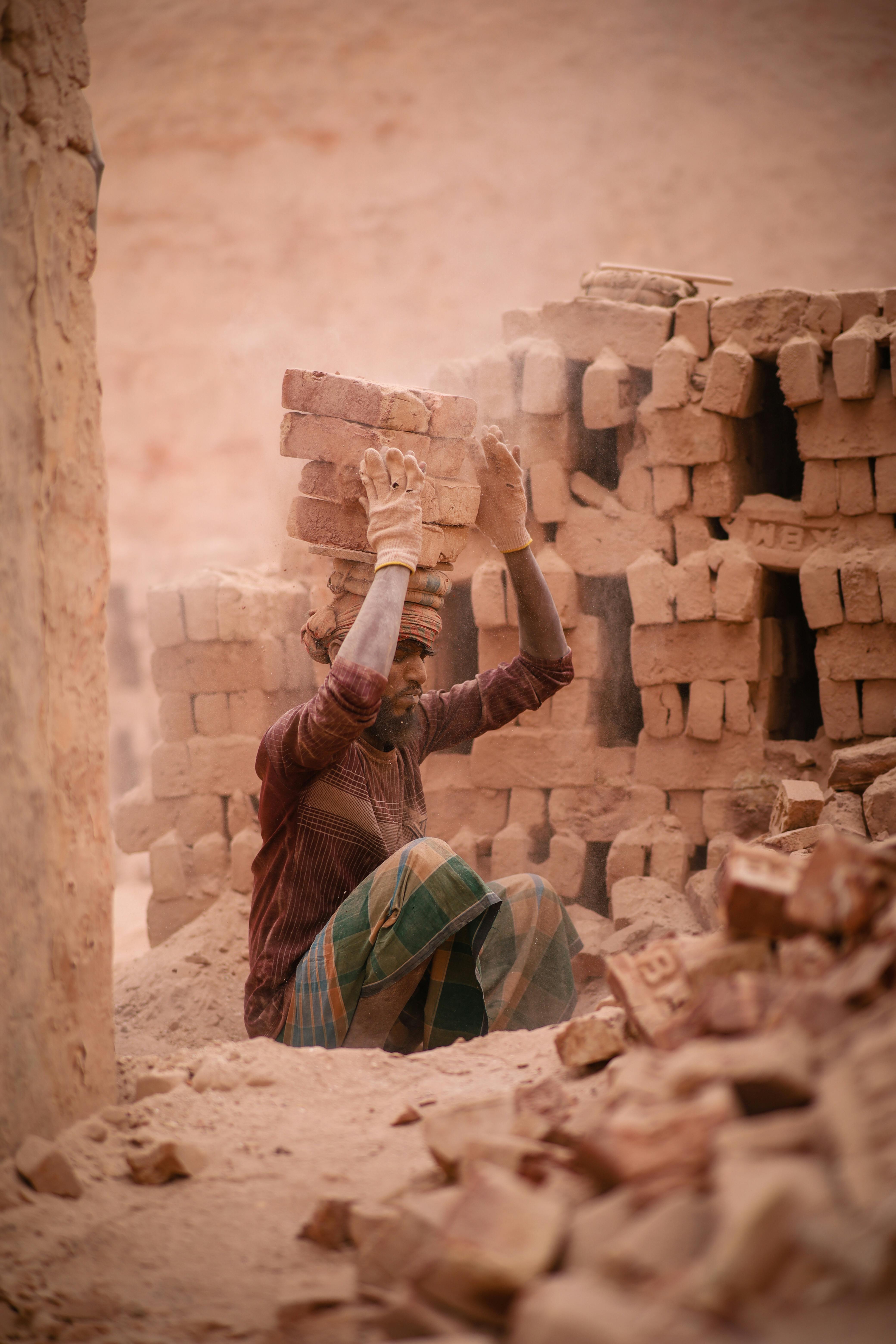 Laborer Carrying Bricks in a Dusty Yard · Free Stock Photo