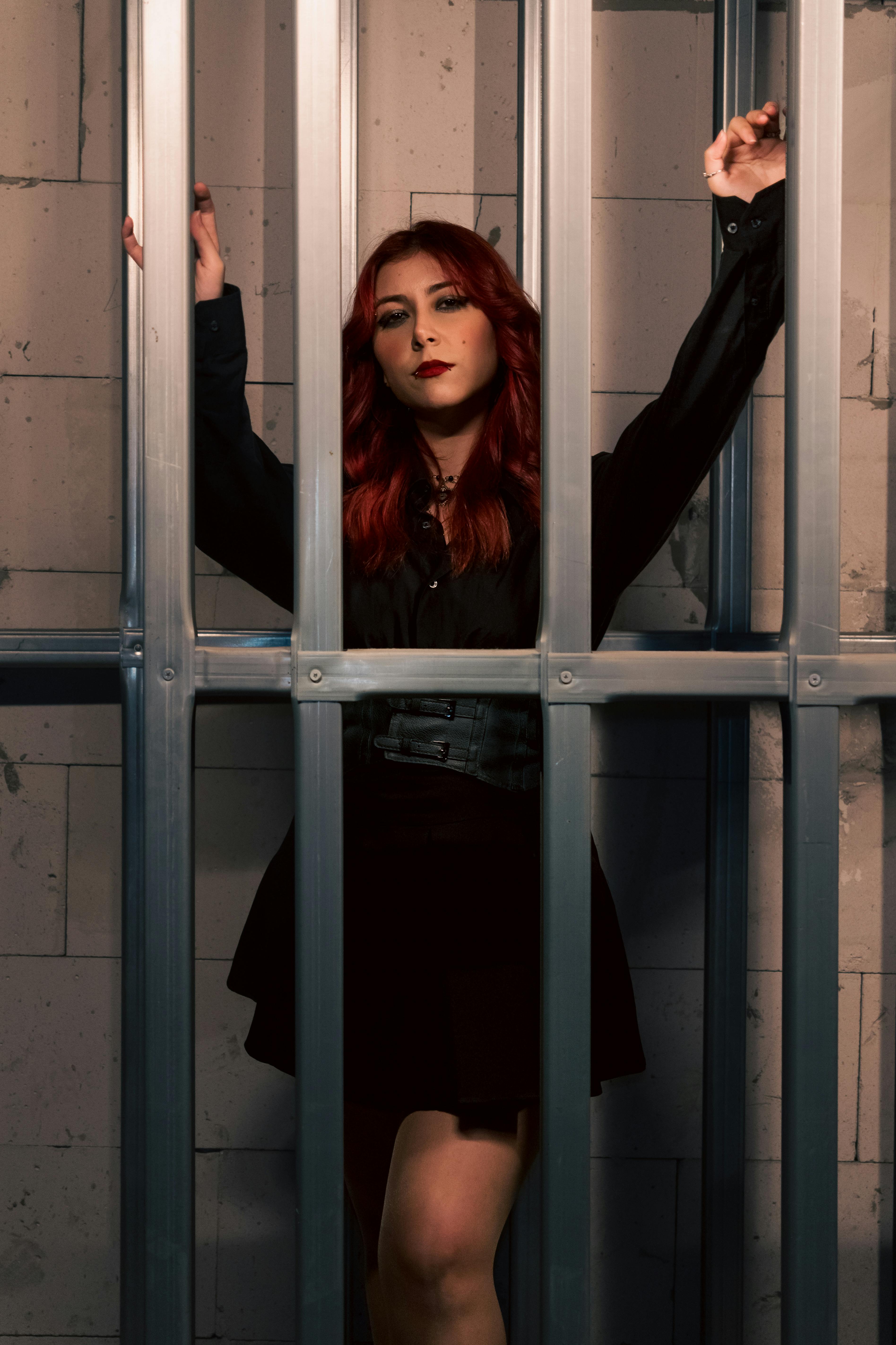 Woman with red hair behind metal bars in moody light · Free Stock Photo