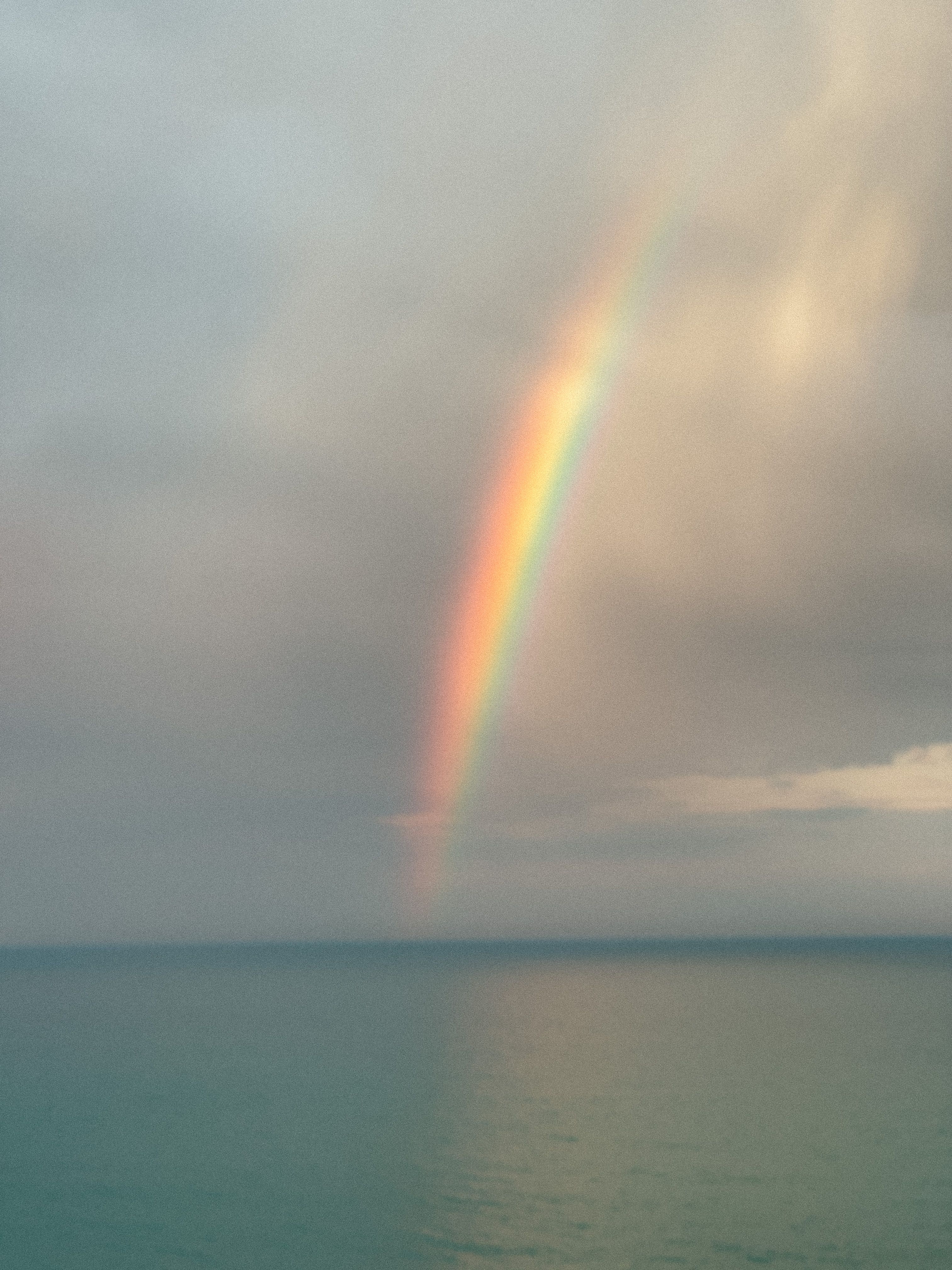 Serene Ocean Rainbow Under Overcast Skies · Free Stock Photo