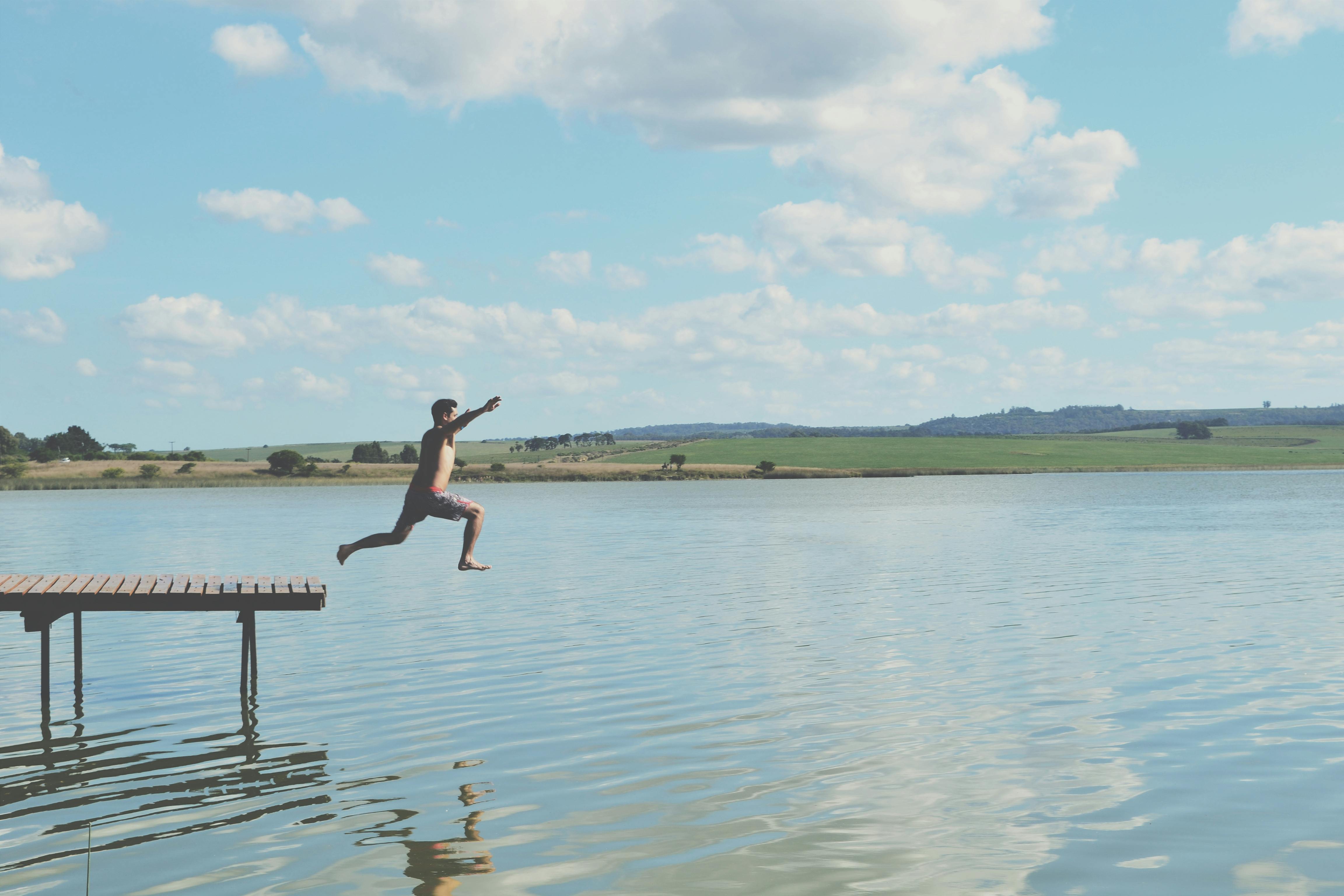 Young Boy Jumping off Pier into Lake · Free Stock Photo