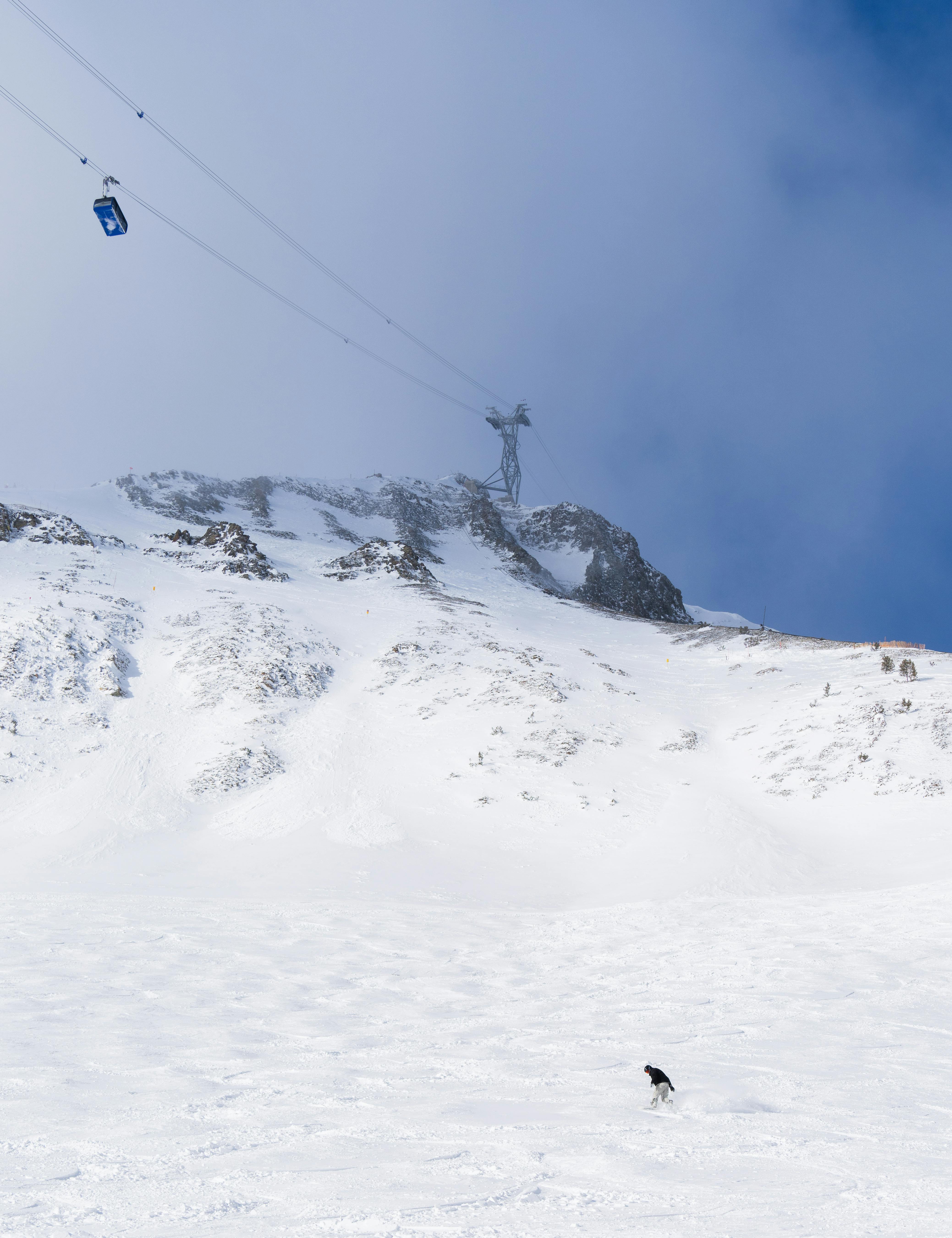 Skier Descending Snowy Mountain with Tram Overhead · Free Stock Photo
