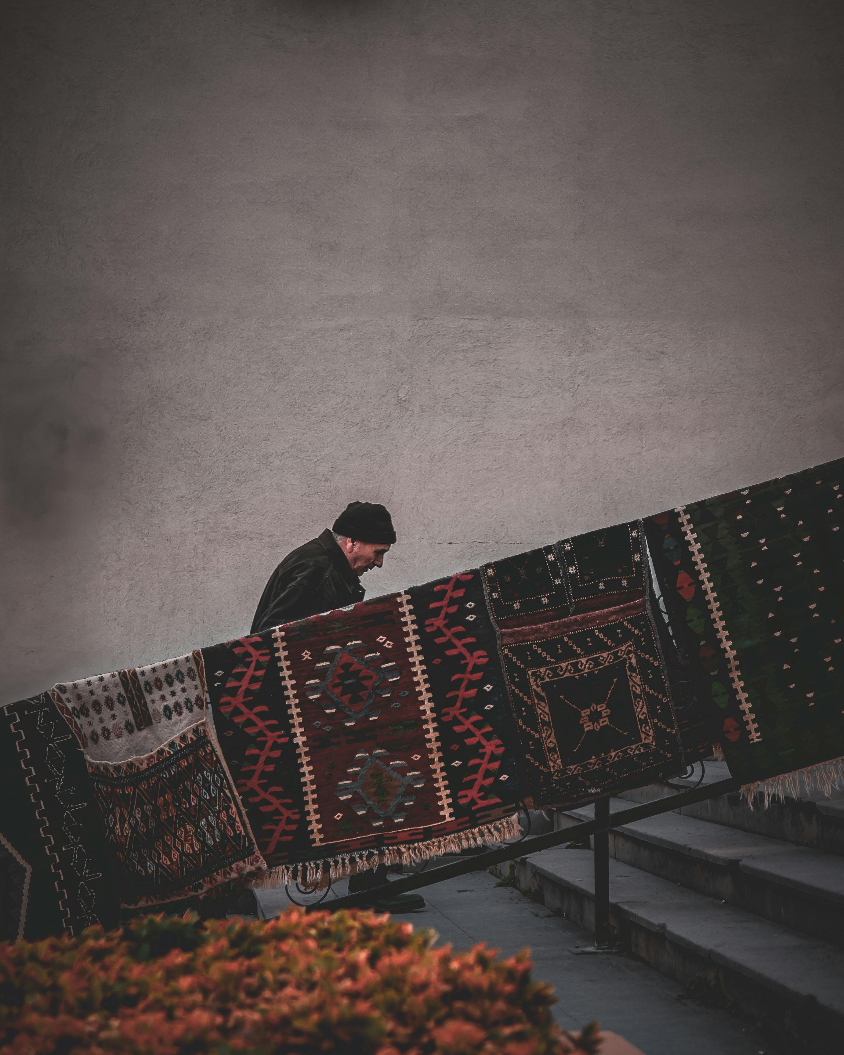 Man Displaying Traditional Rugs Along Urban Street · Free Stock Photo